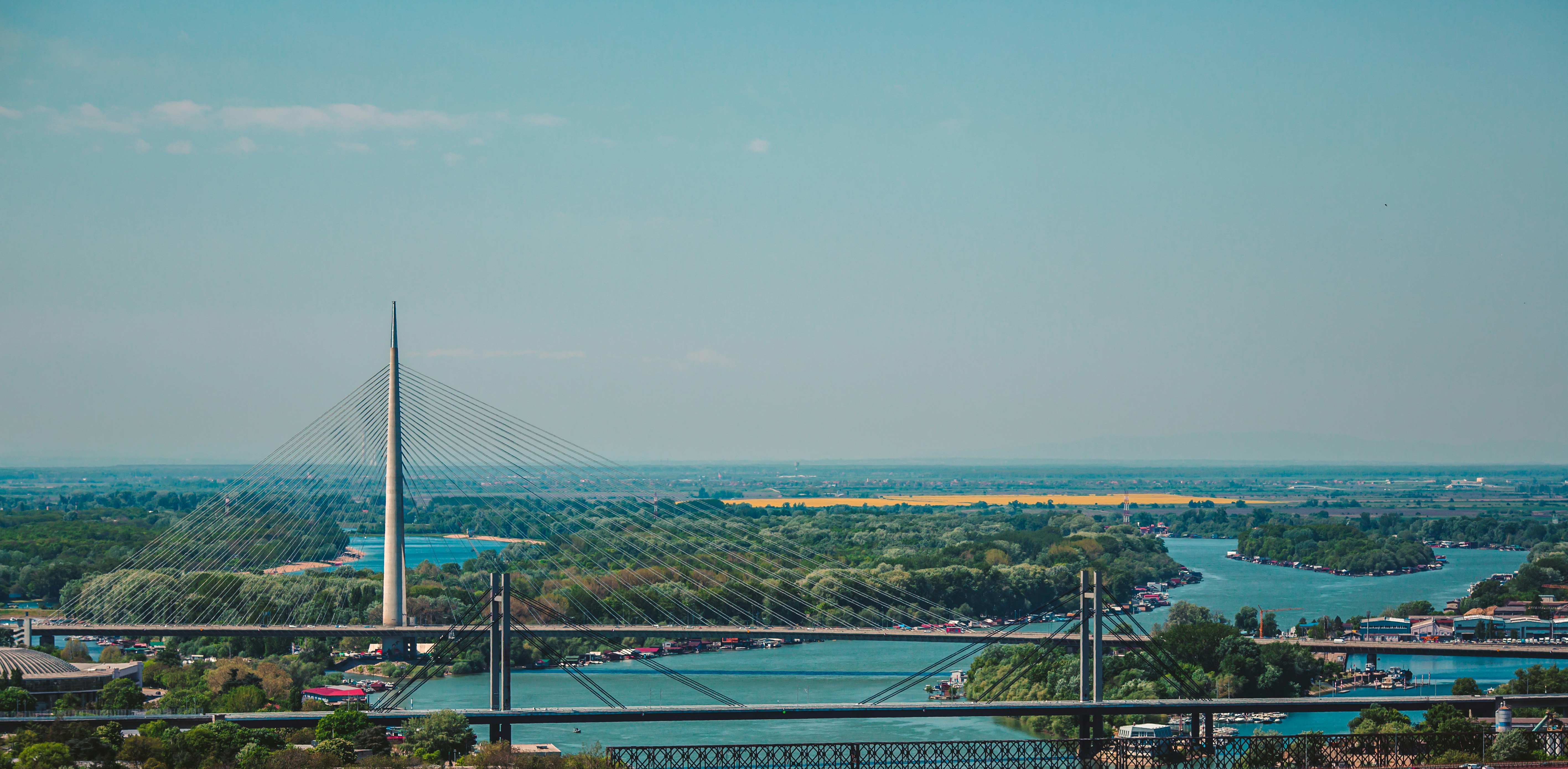 Bridge spanning a tranquil river surrounded by lush greenery under a clear blue sky.
