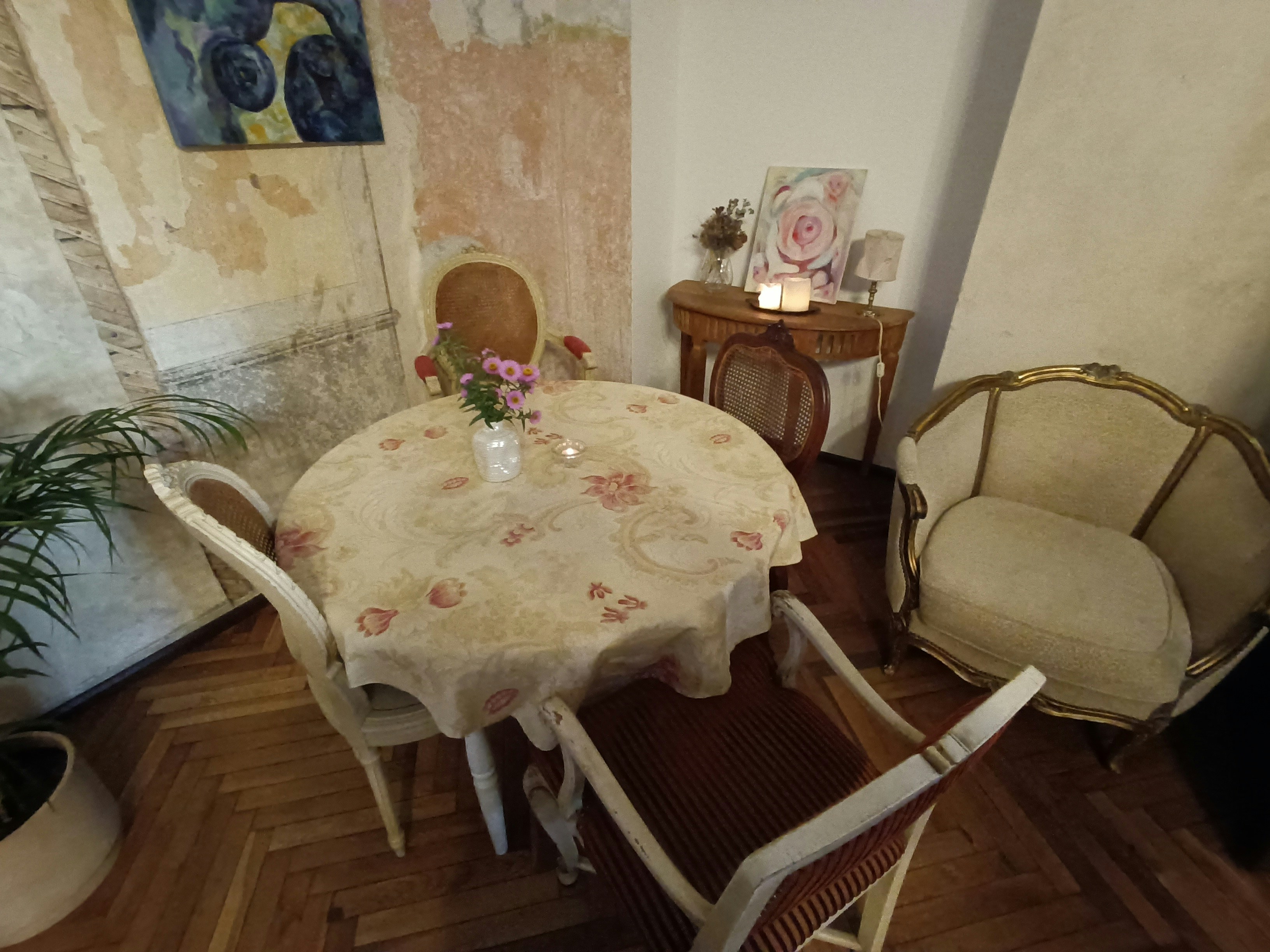 Charming dining area featuring a floral tablecloth, a vase of flowers, and vintage furniture against a textured wall. Soft lighting enhances the inviting atmosphere.