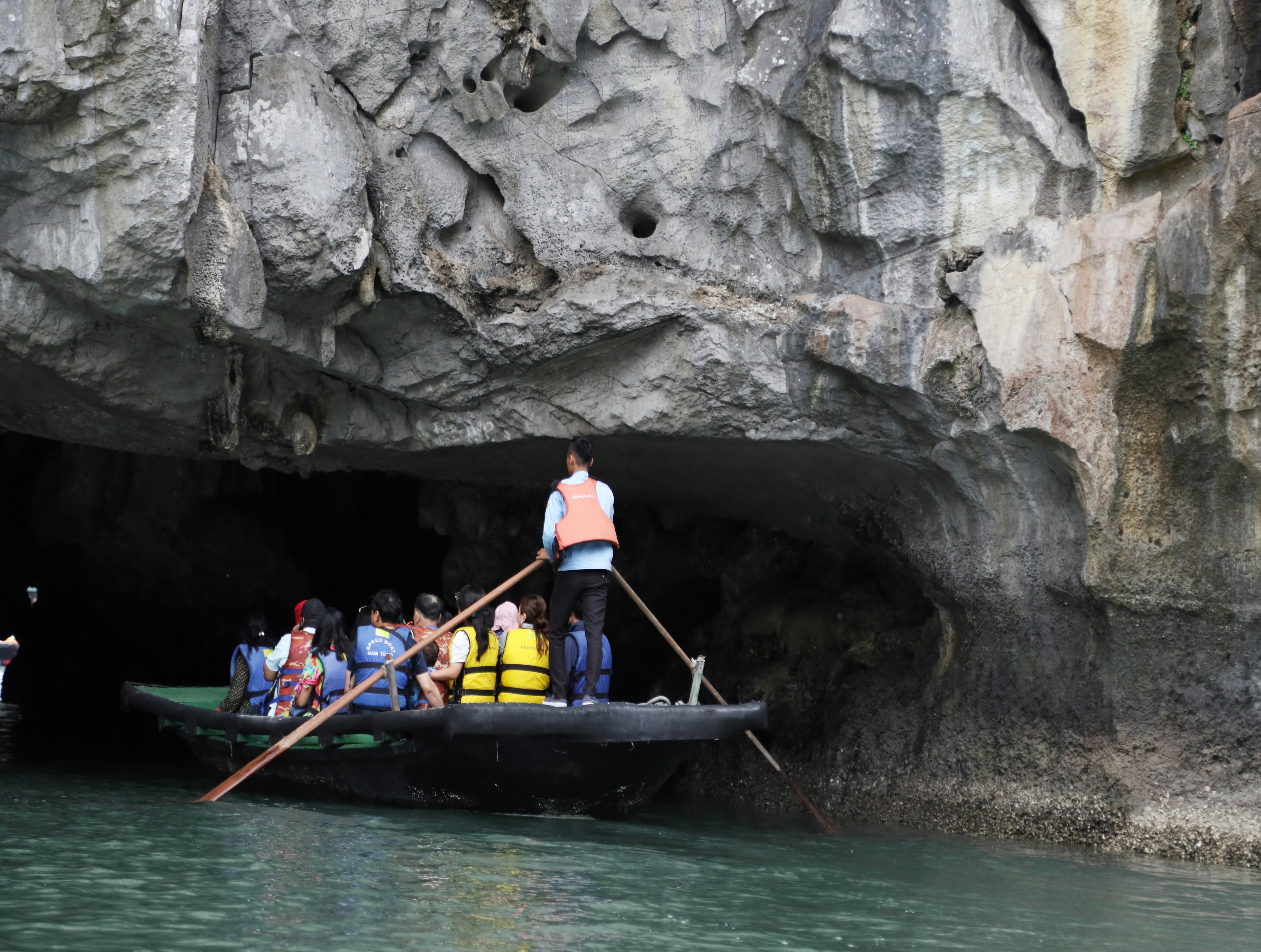 Crew on a raft threads turquoise water into a shadowed sea cave