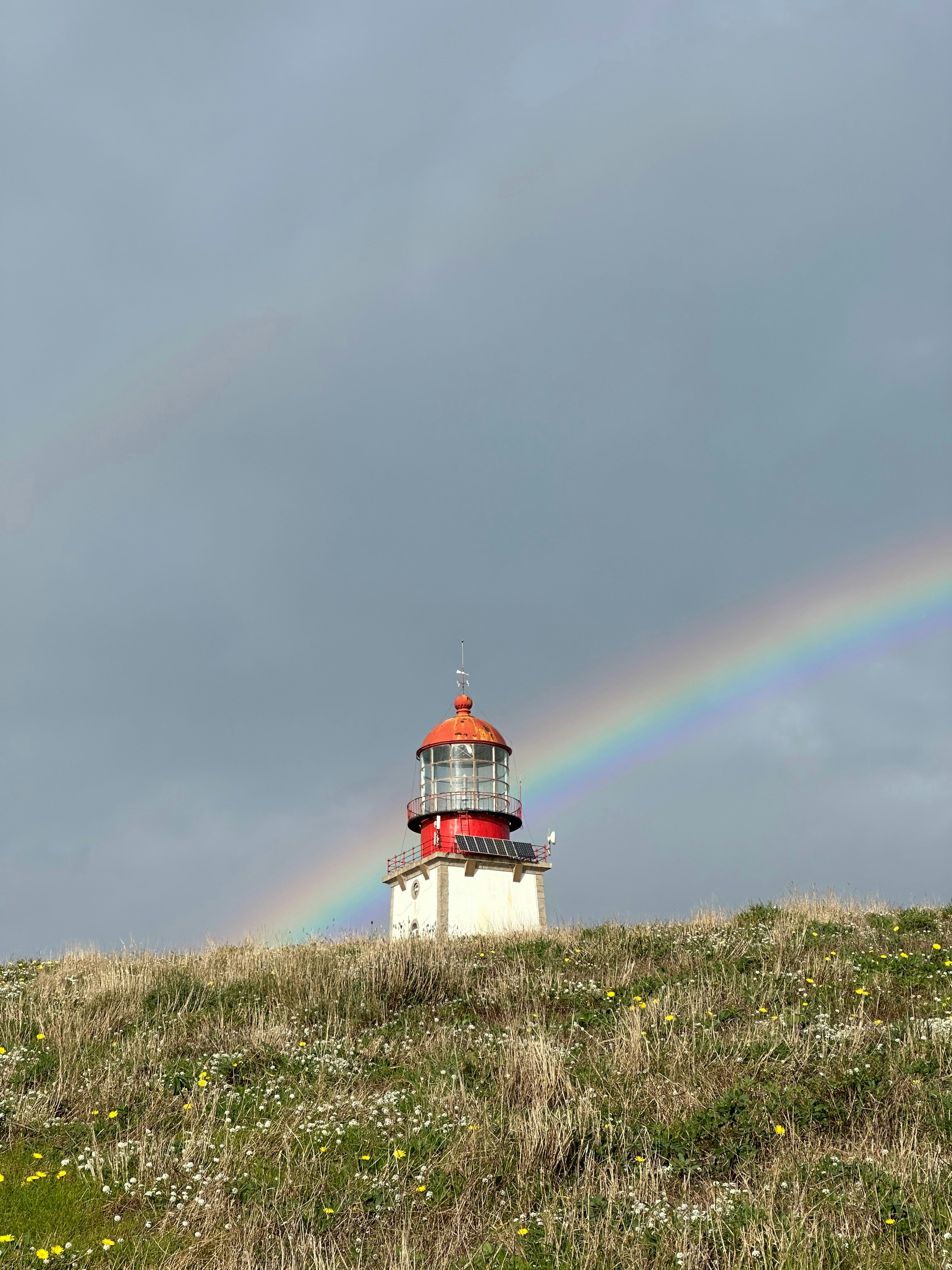Rainbow Arch Over the Red-Capped Lighthouse on a Grassy Dune