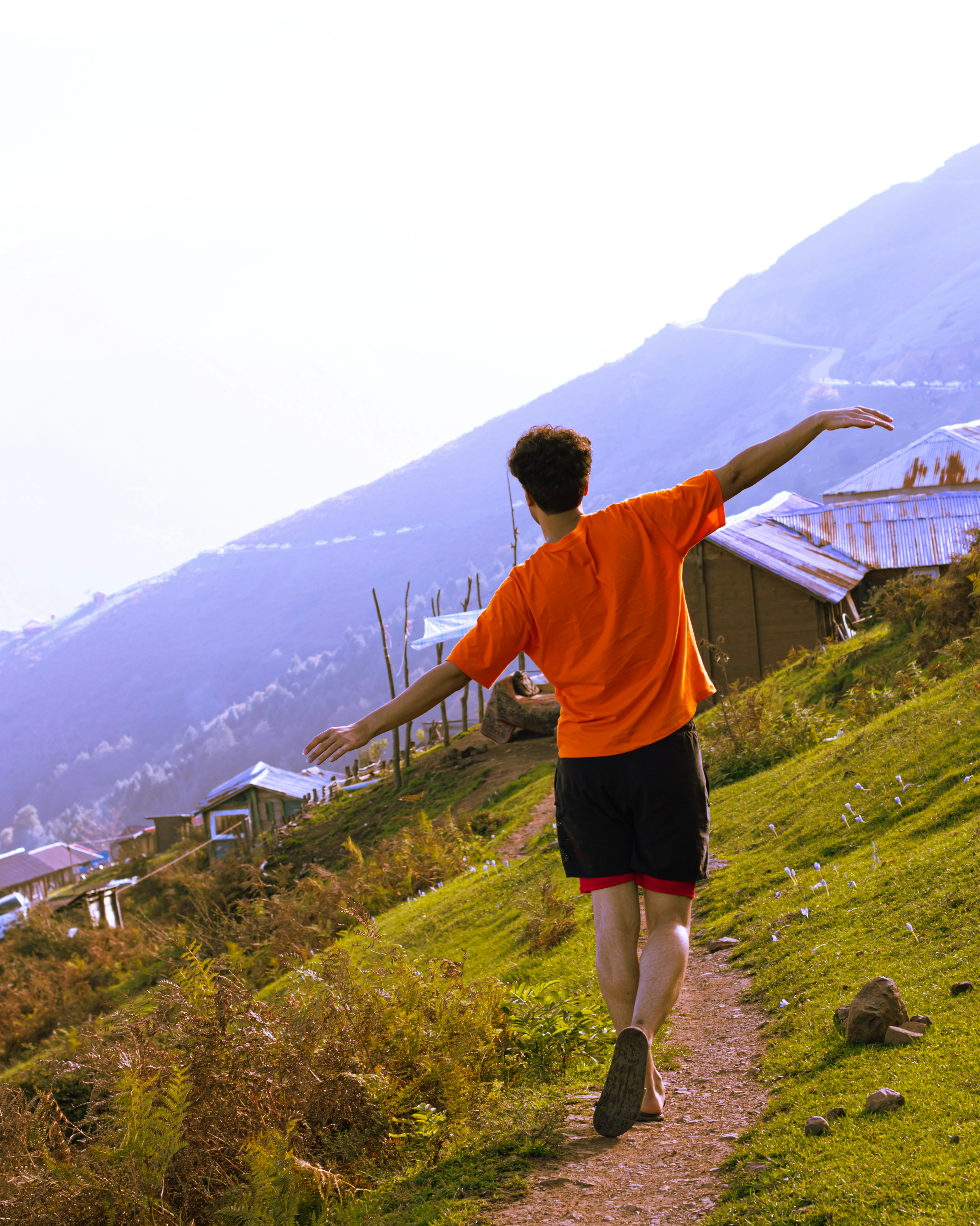Balancing on a hillside trail under a vivid orange shirt