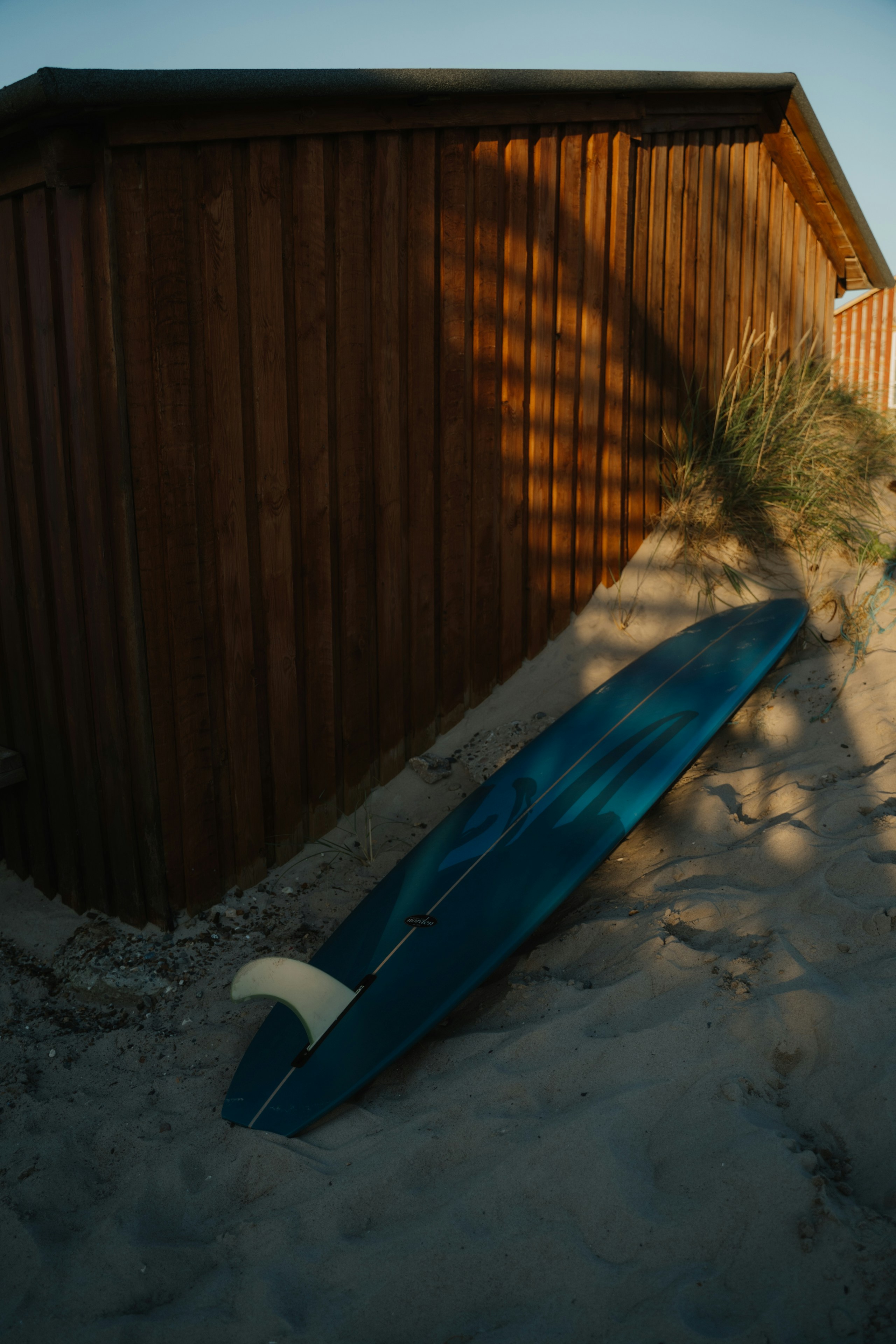 A blue surfboard laying in the sand next to a building photo – Free ...