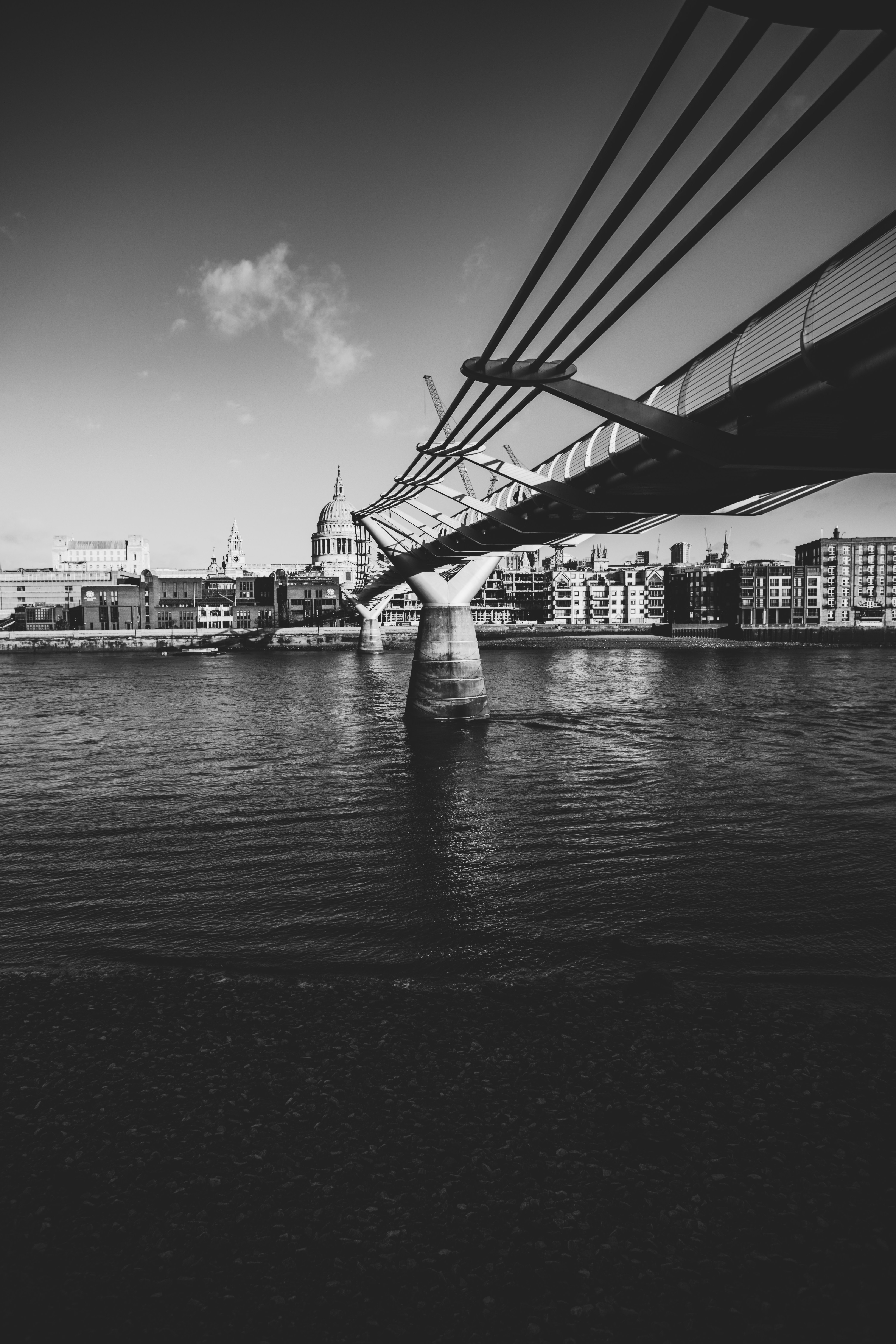 A modern bridge arches gracefully over the river, framed by historic buildings in the background. The monochrome palette enhances the dramatic contrast between structure and water.