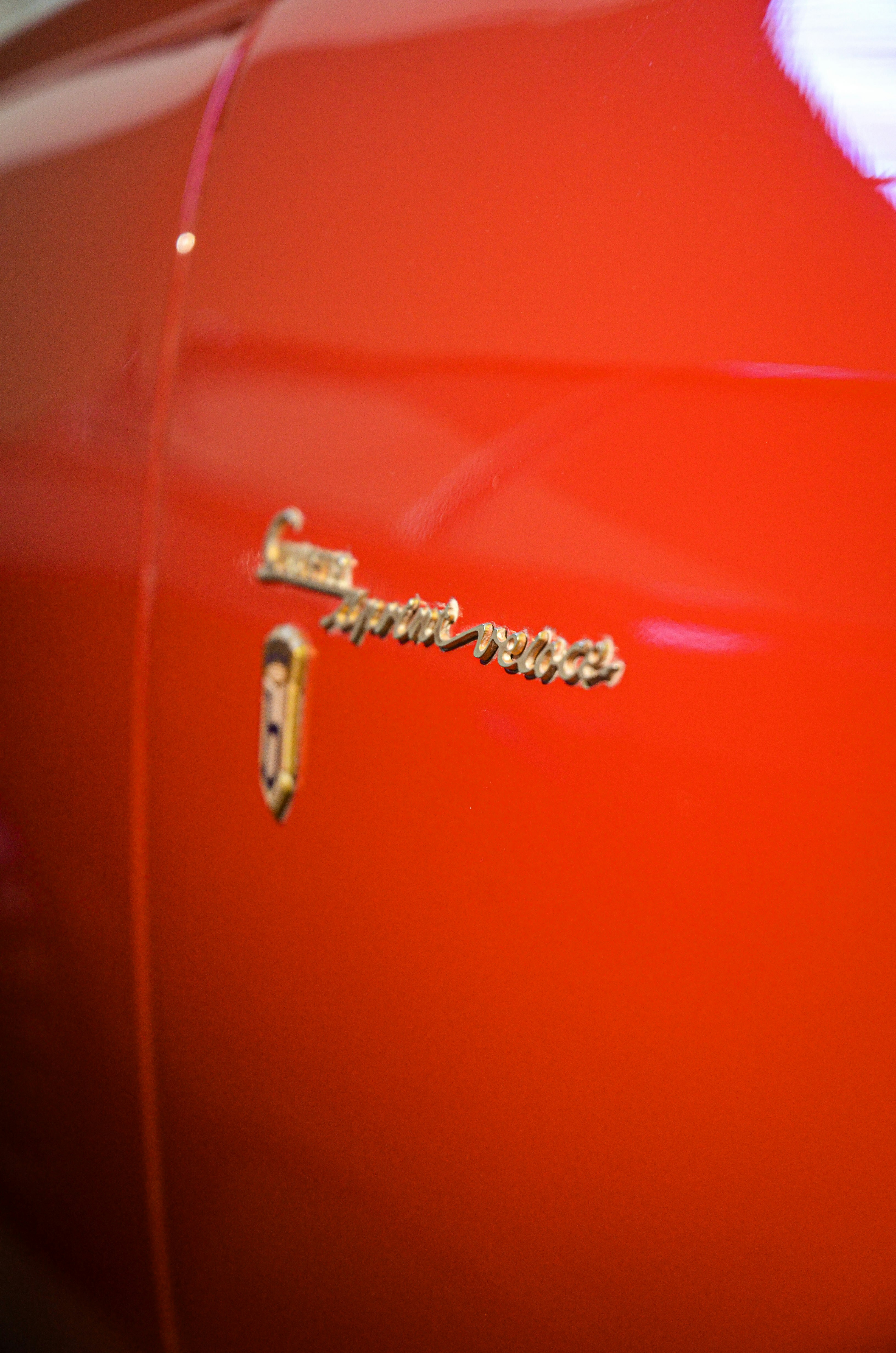 Scarlet Curve: Chrome Script Badge on a Classic Car Panel