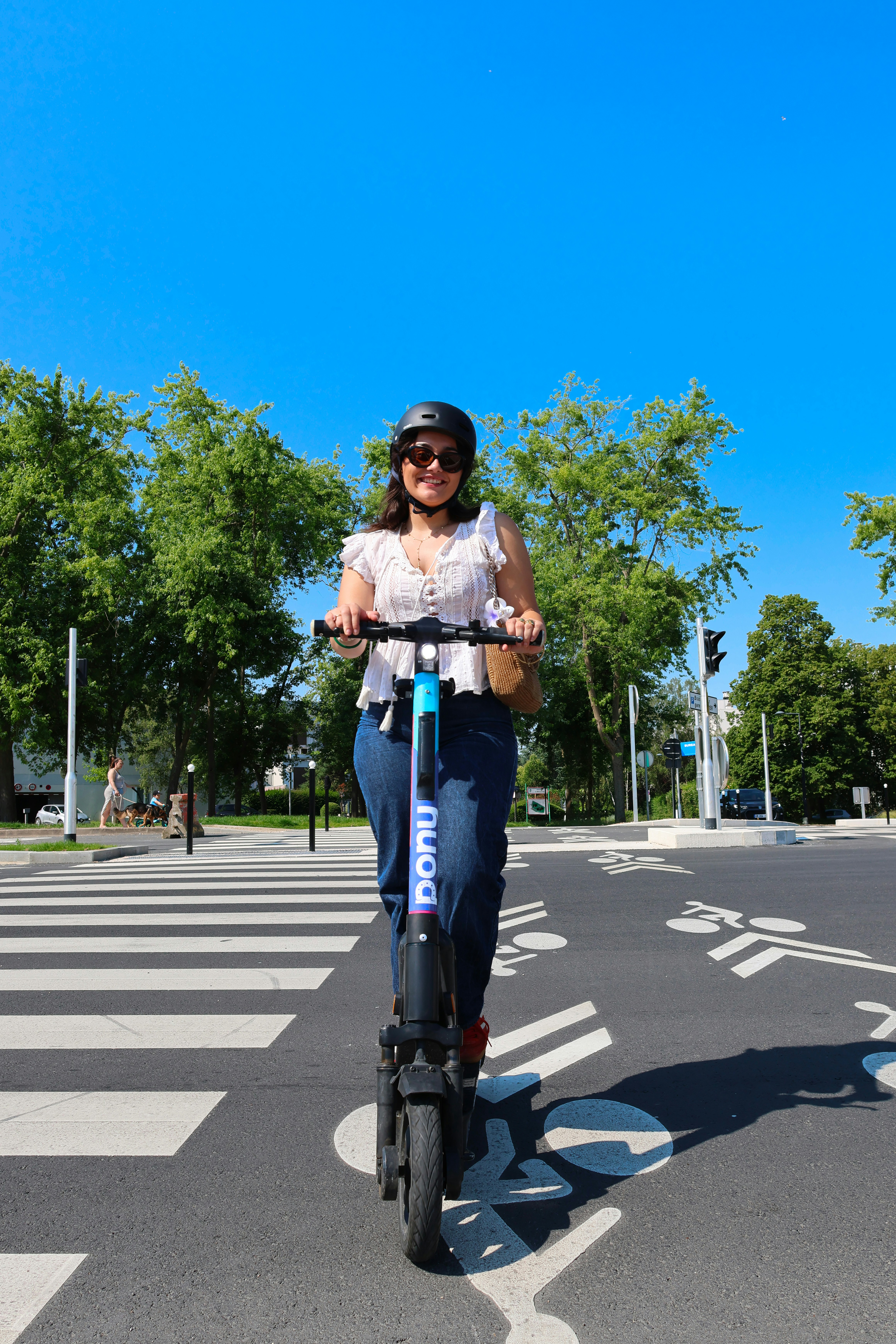 A woman riding a scooter across a street photo – Free Évry ...