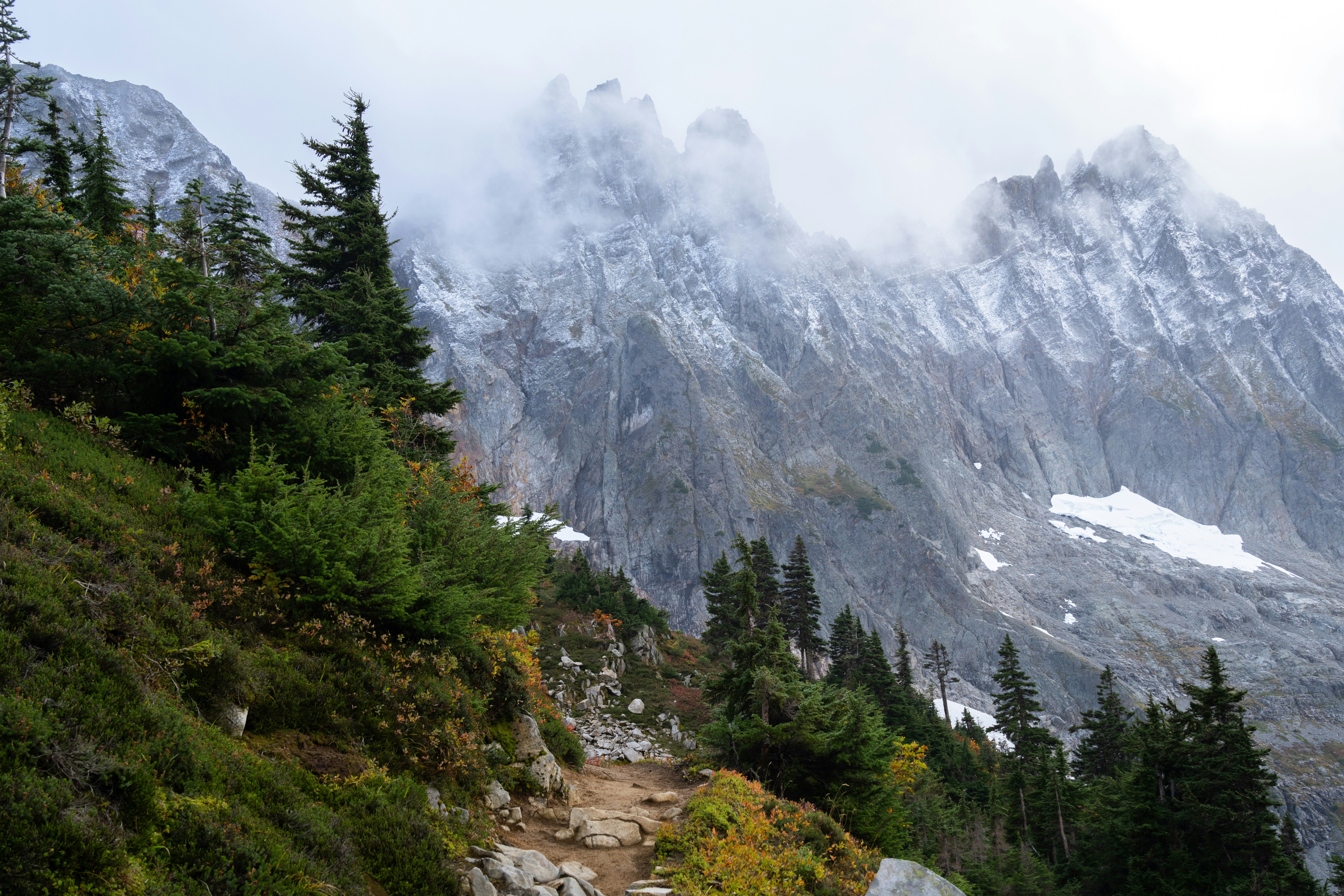 A trail leading up a mountain with snow covered mountains in the background