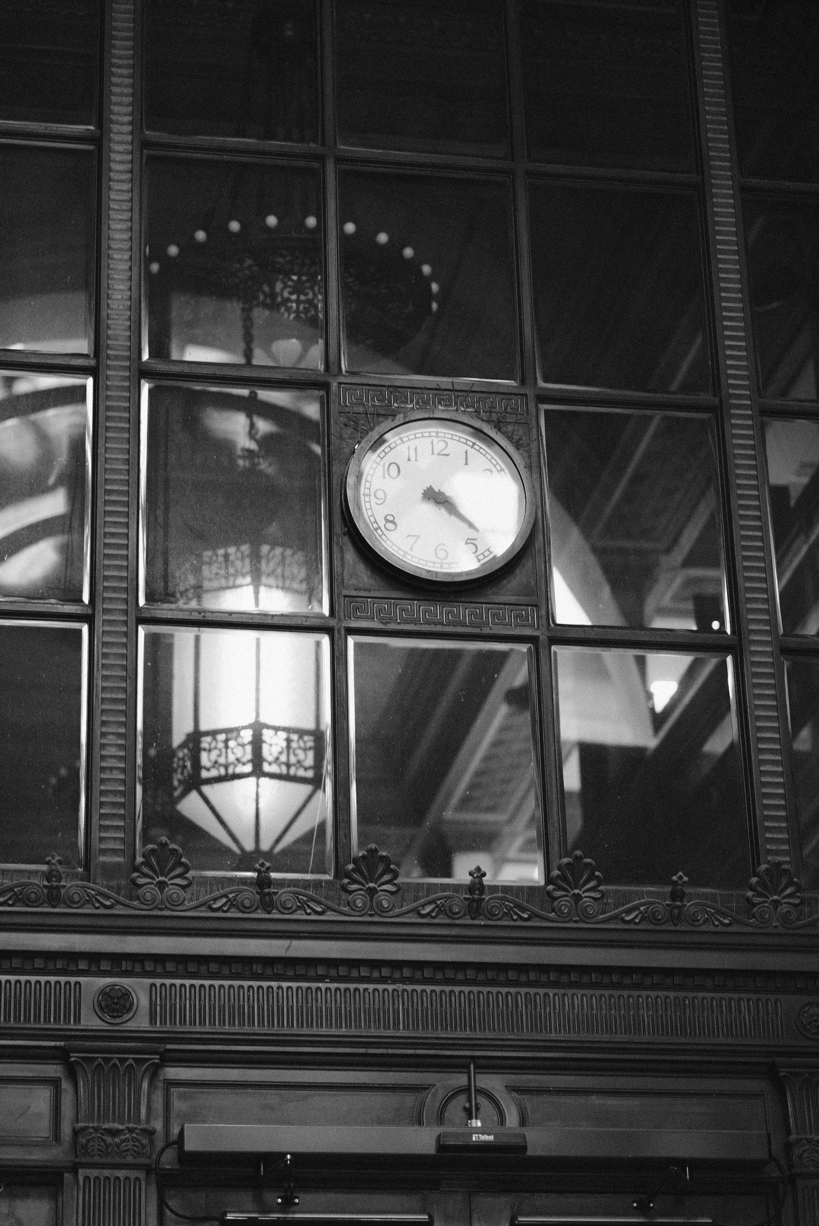 Timeless Clock Behind Glass: An Ornate Facade and Hanging Light Reflections
