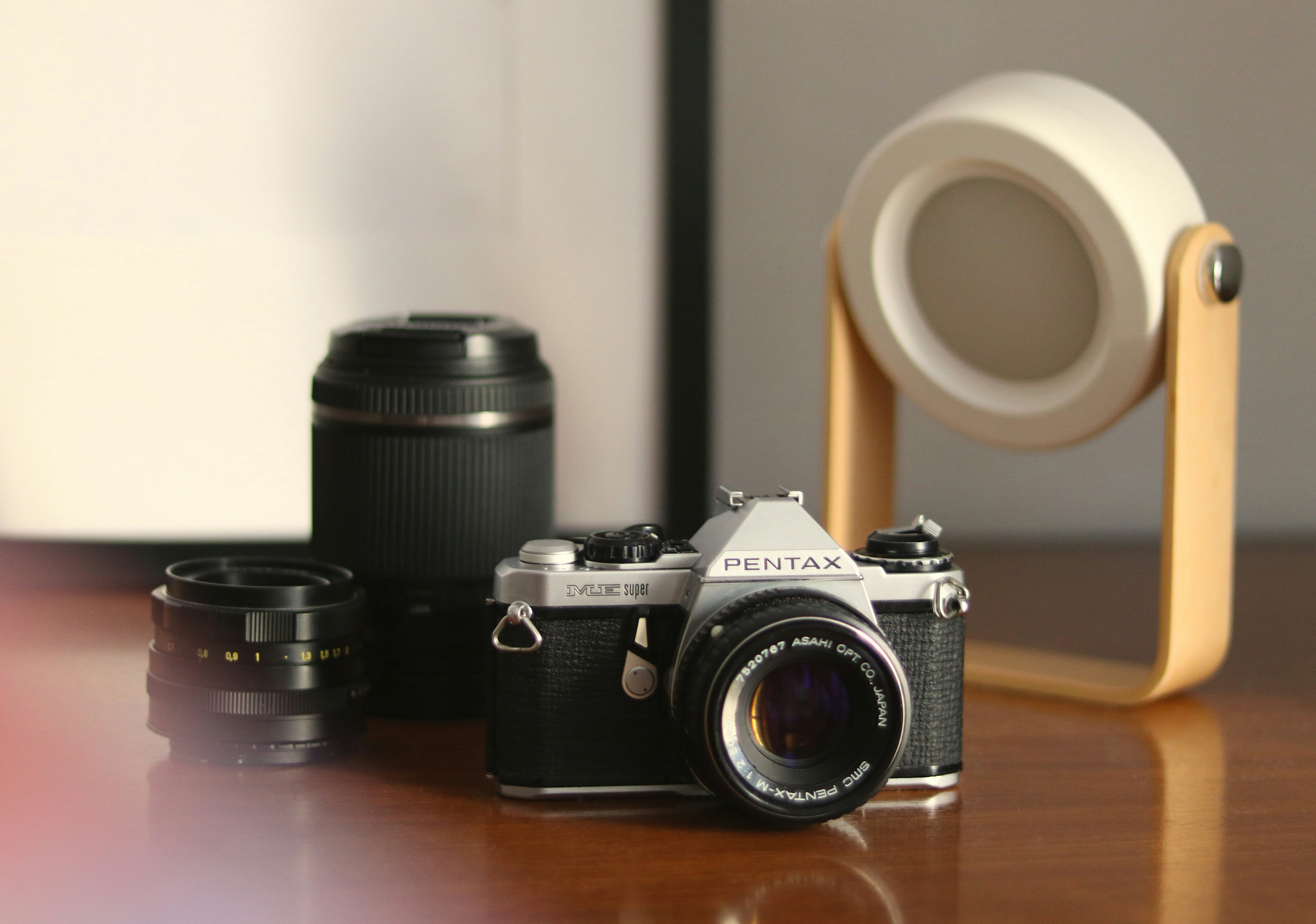 Classic Pentax camera surrounded by modern lenses and a minimalist lamp, showcasing a blend of photography history and contemporary design.