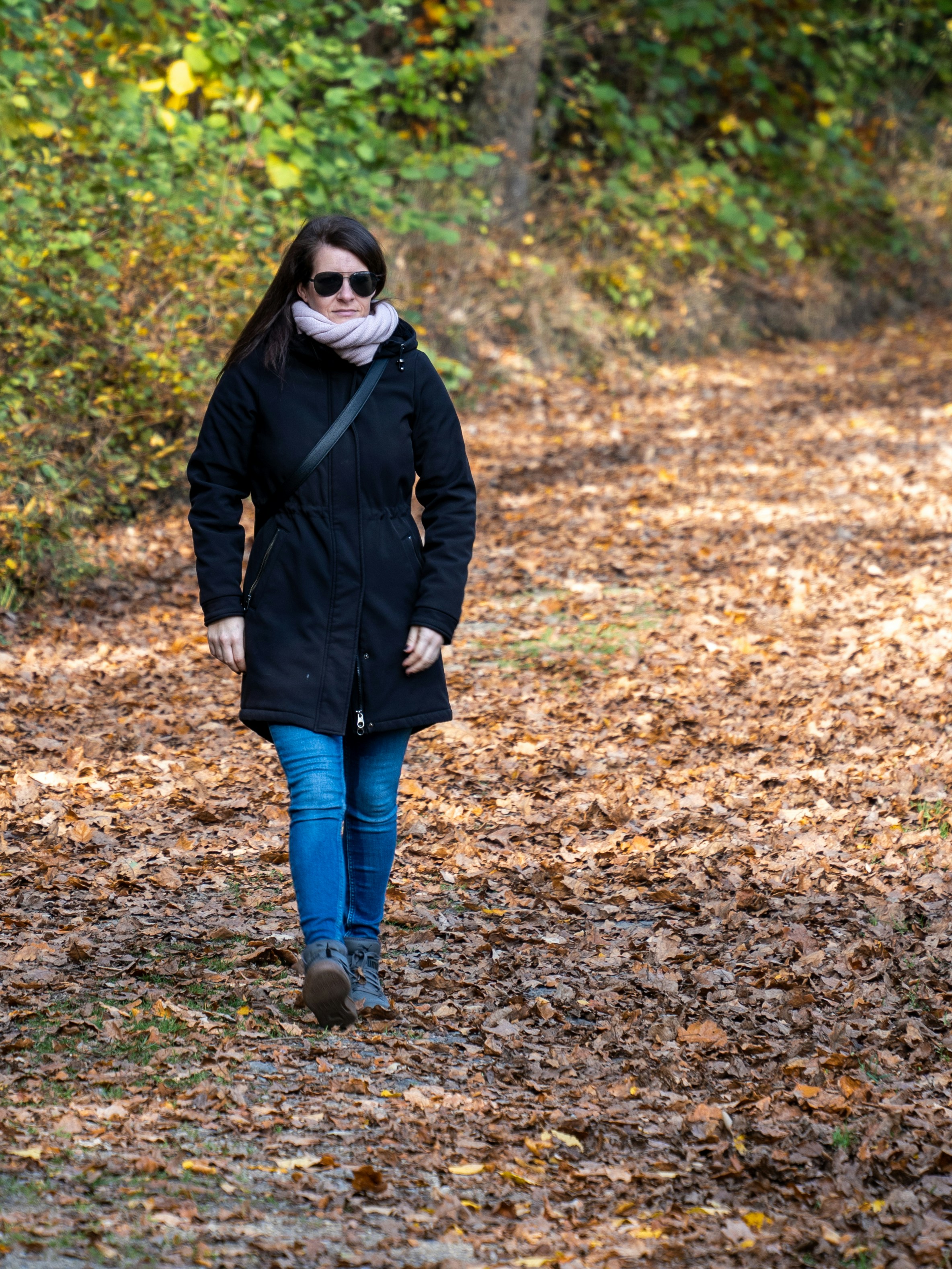 Woman walking a leaf-strewn forest path in autumn warmth