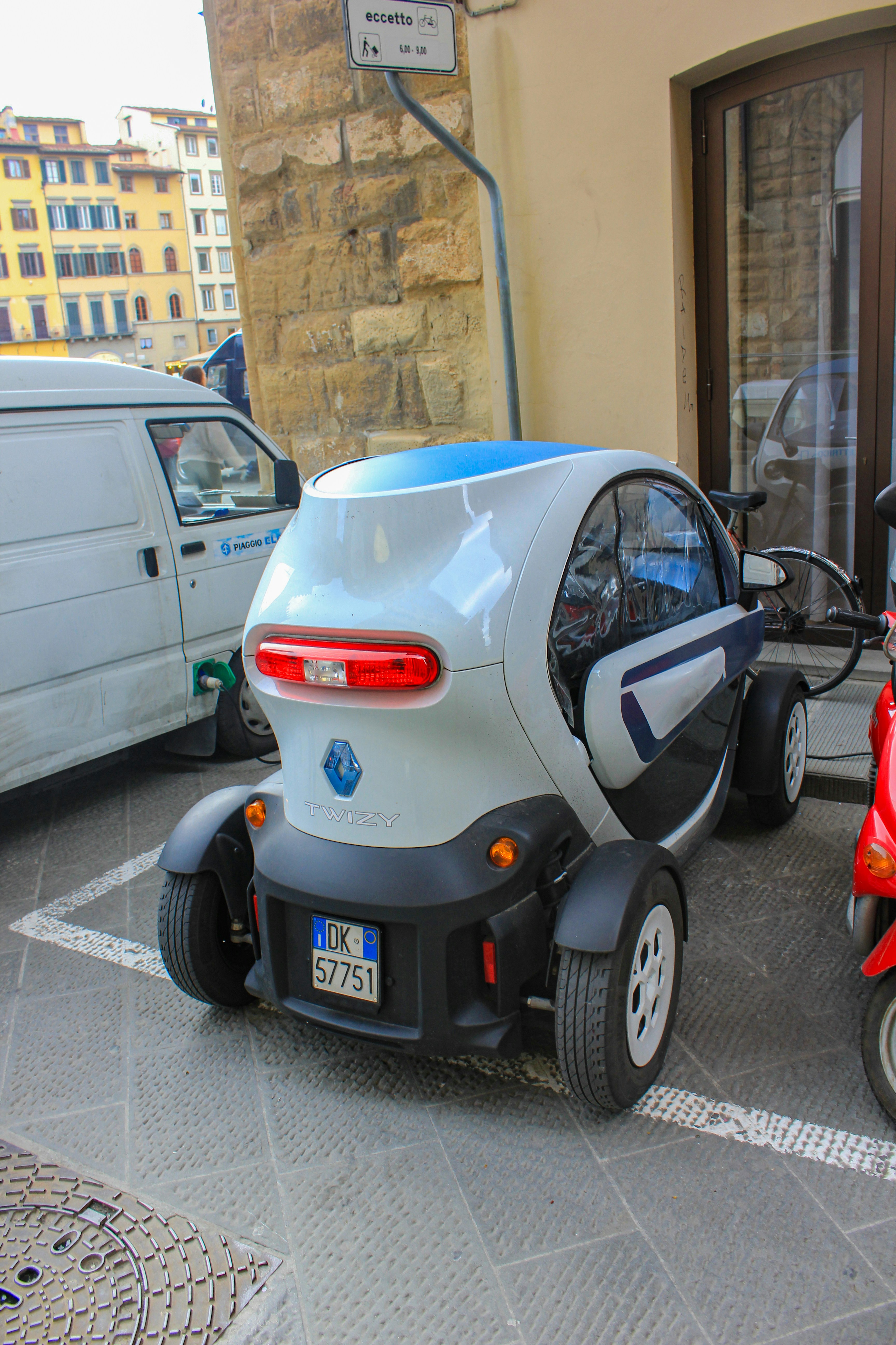 Twizy on a sunlit European street, framed by stone and a waiting van
