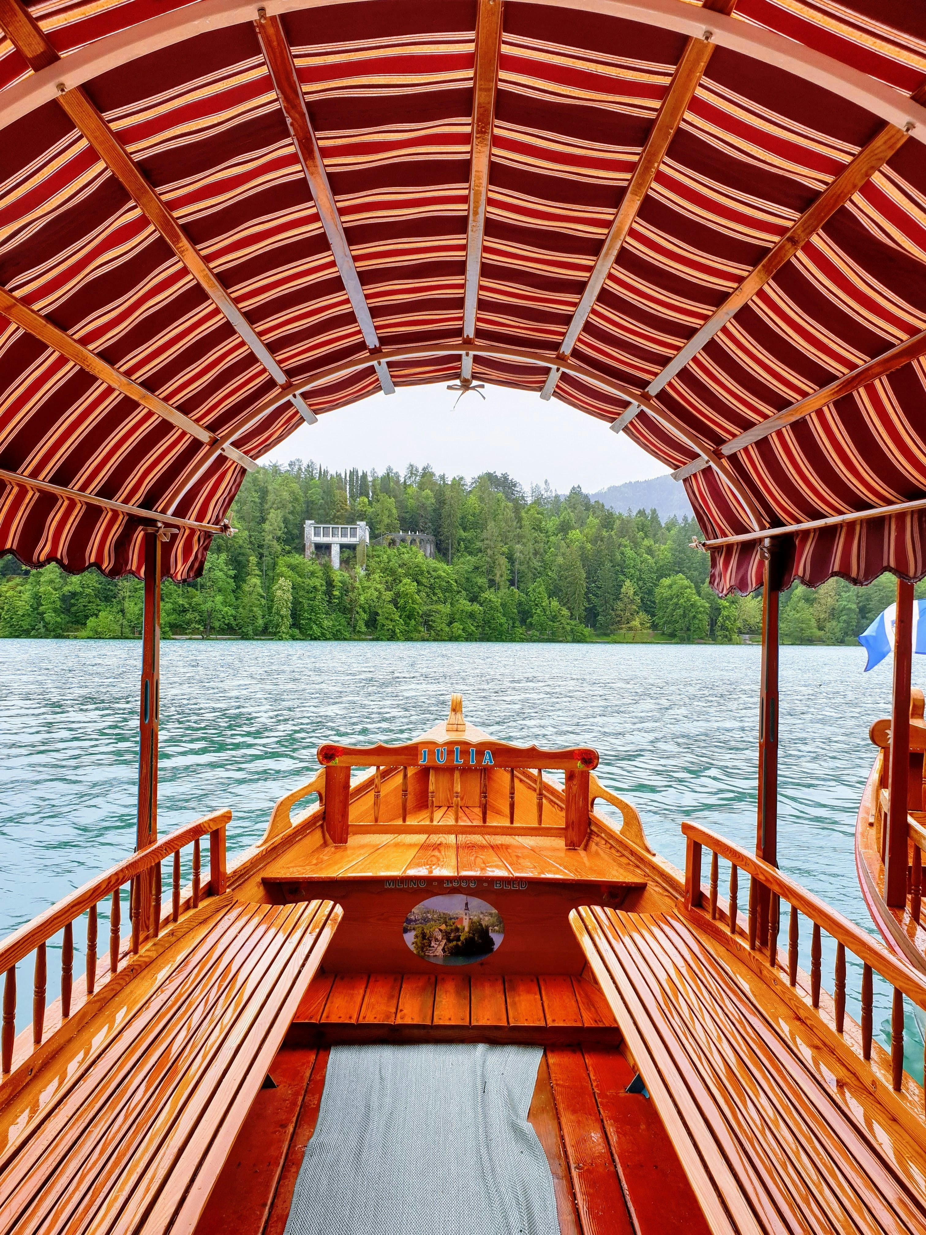Symmetrical wooden boat interior with striped canopy framing a calm lake and green hillside beyond.