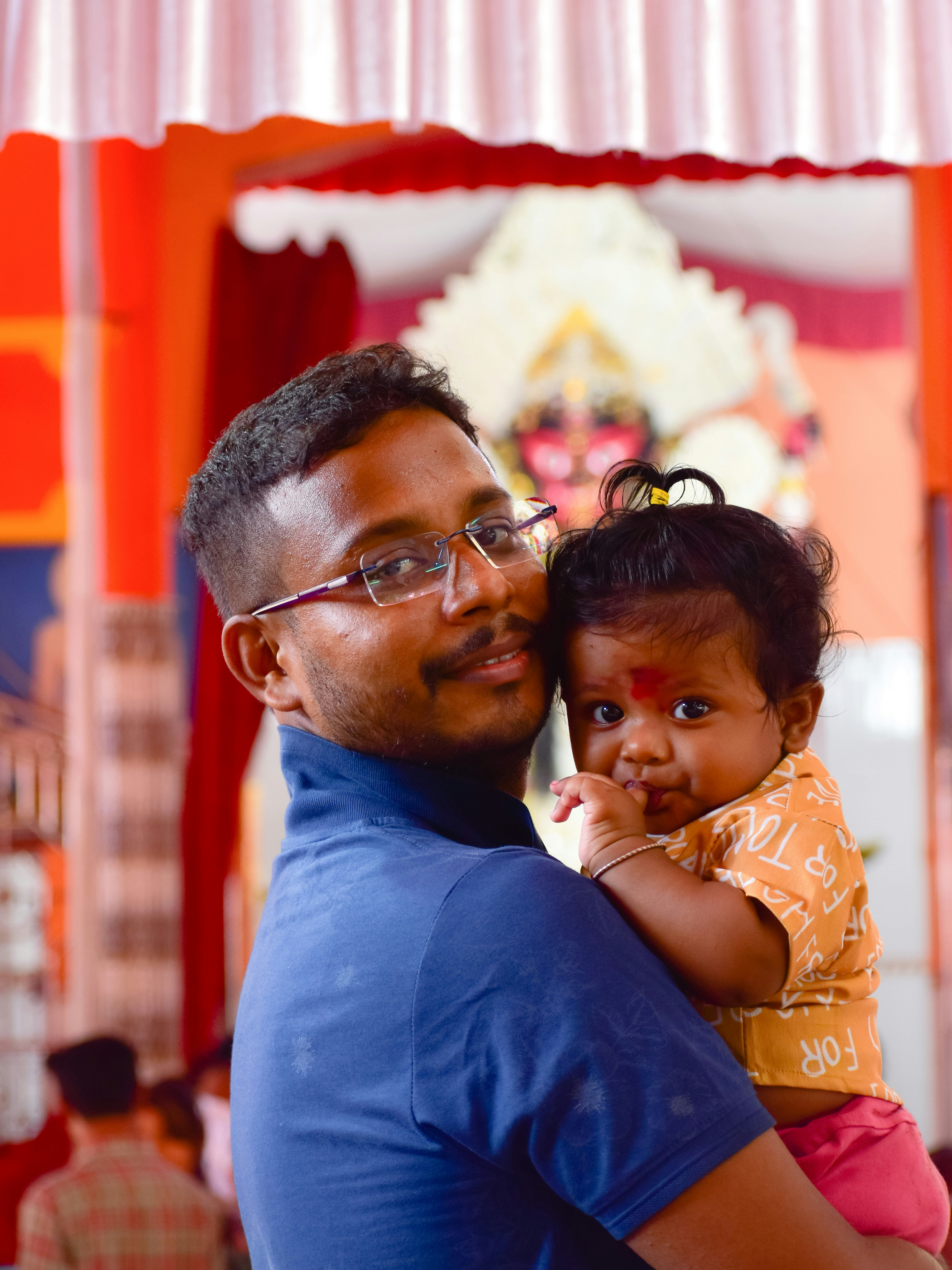 Holding Hope: A Father and Daughter Beside a Shrine’s Orange Curtain