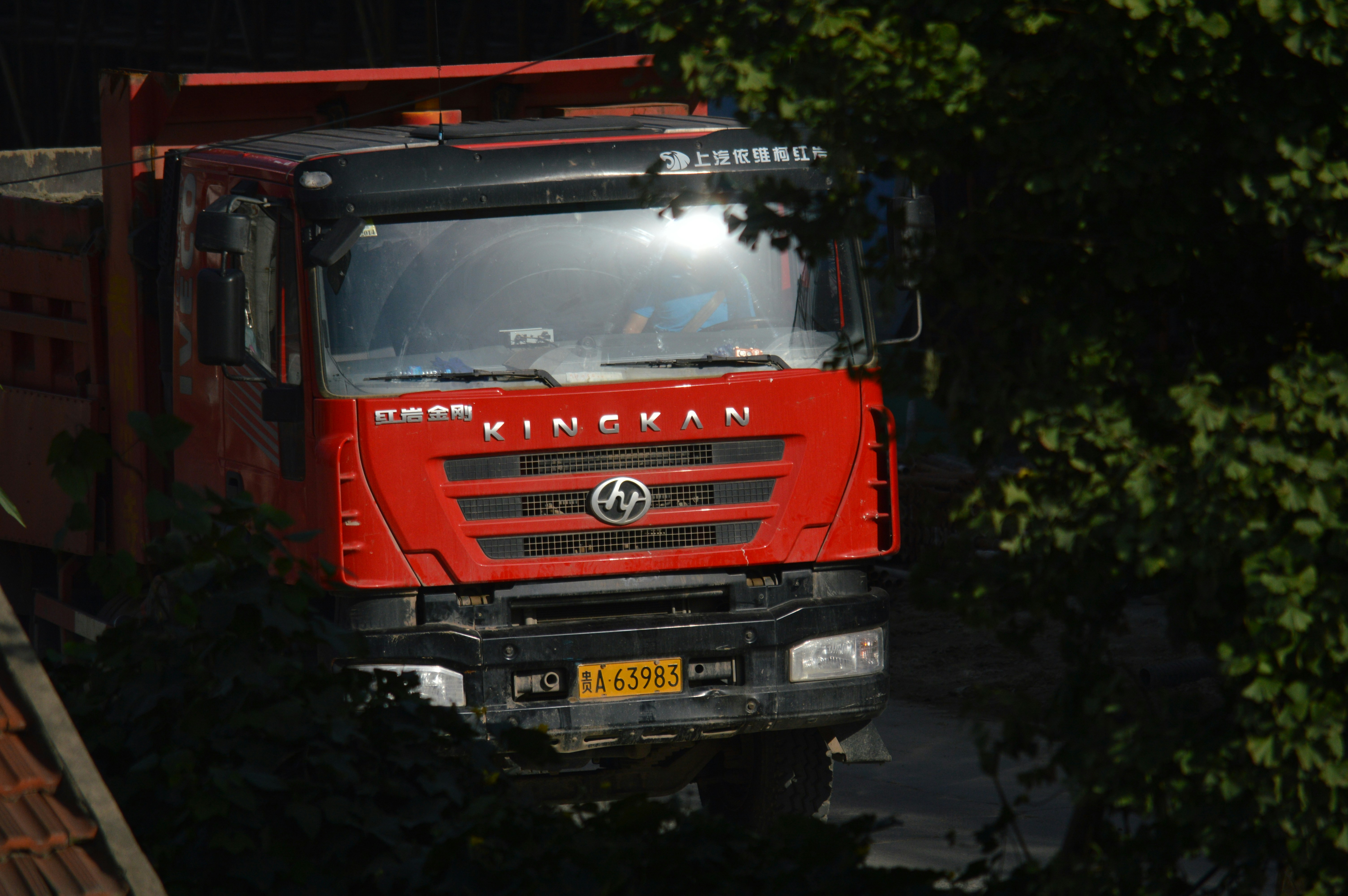 Front-View Red Kingkan Truck Emerging from Shadow on a Quiet Road