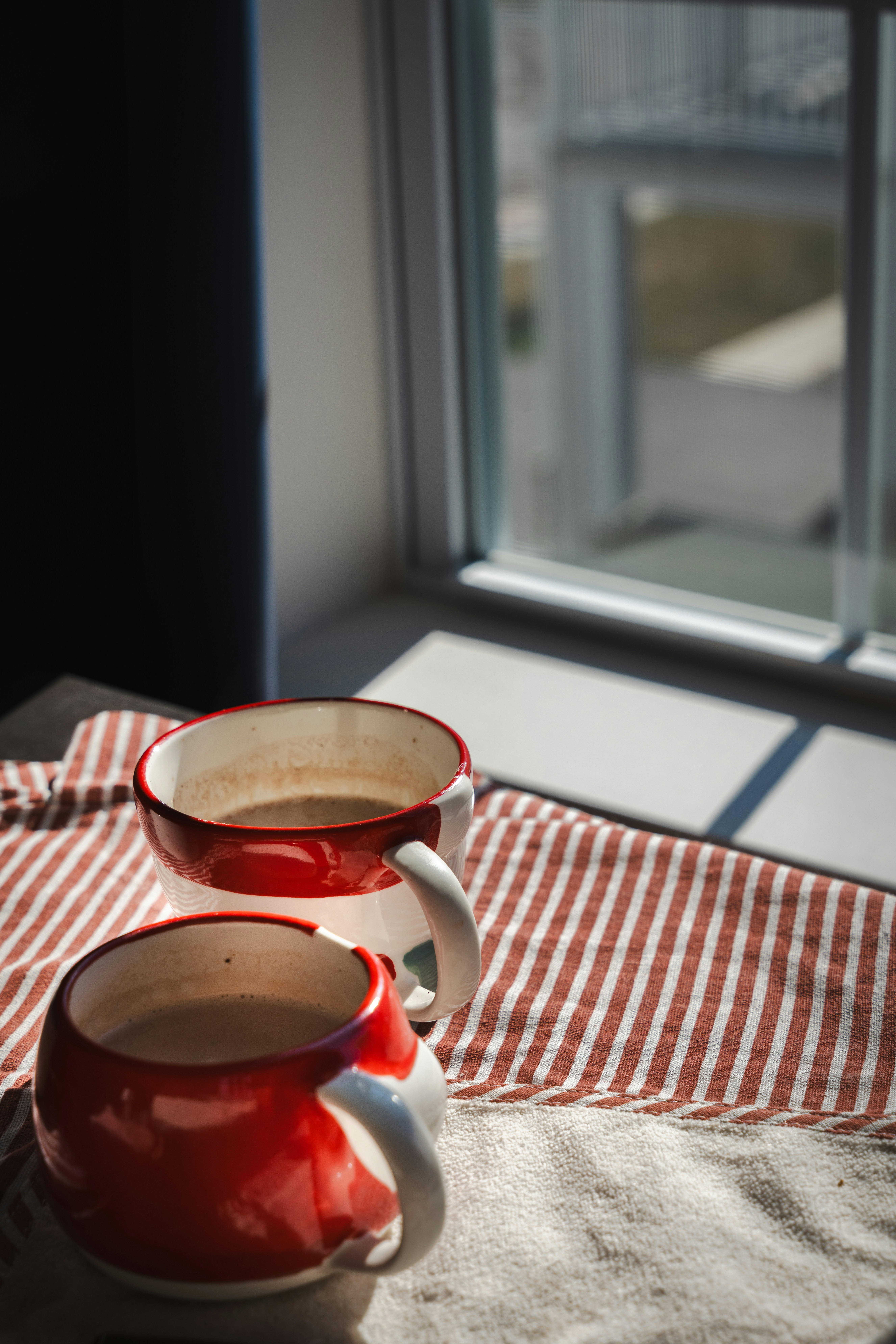 Crimson Dawn: Two Red Mugs on a Sunlit Window Table