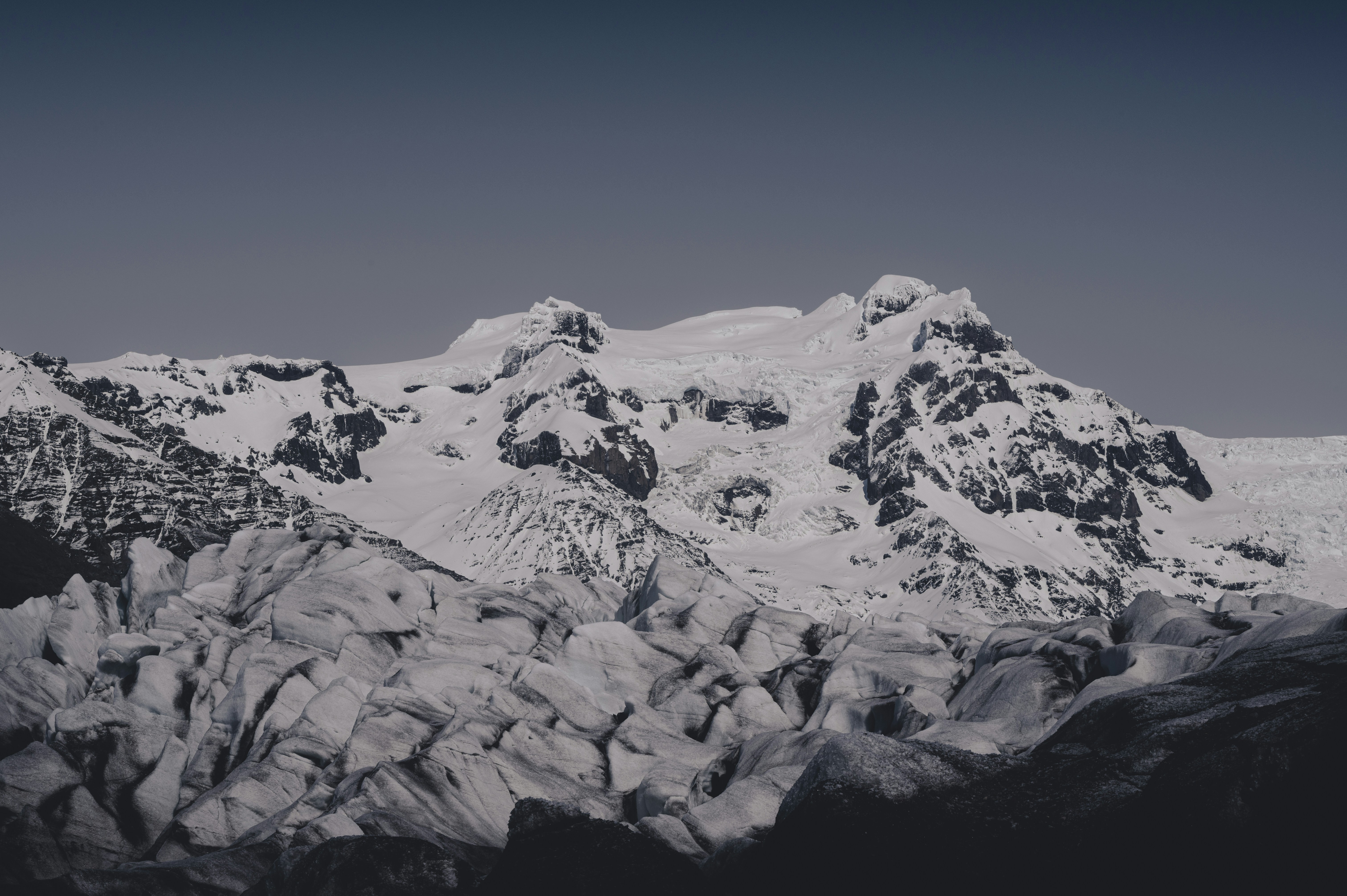 Snow-covered peaks rise majestically above a textured glacier landscape, showcasing the raw beauty of nature's icy formations.