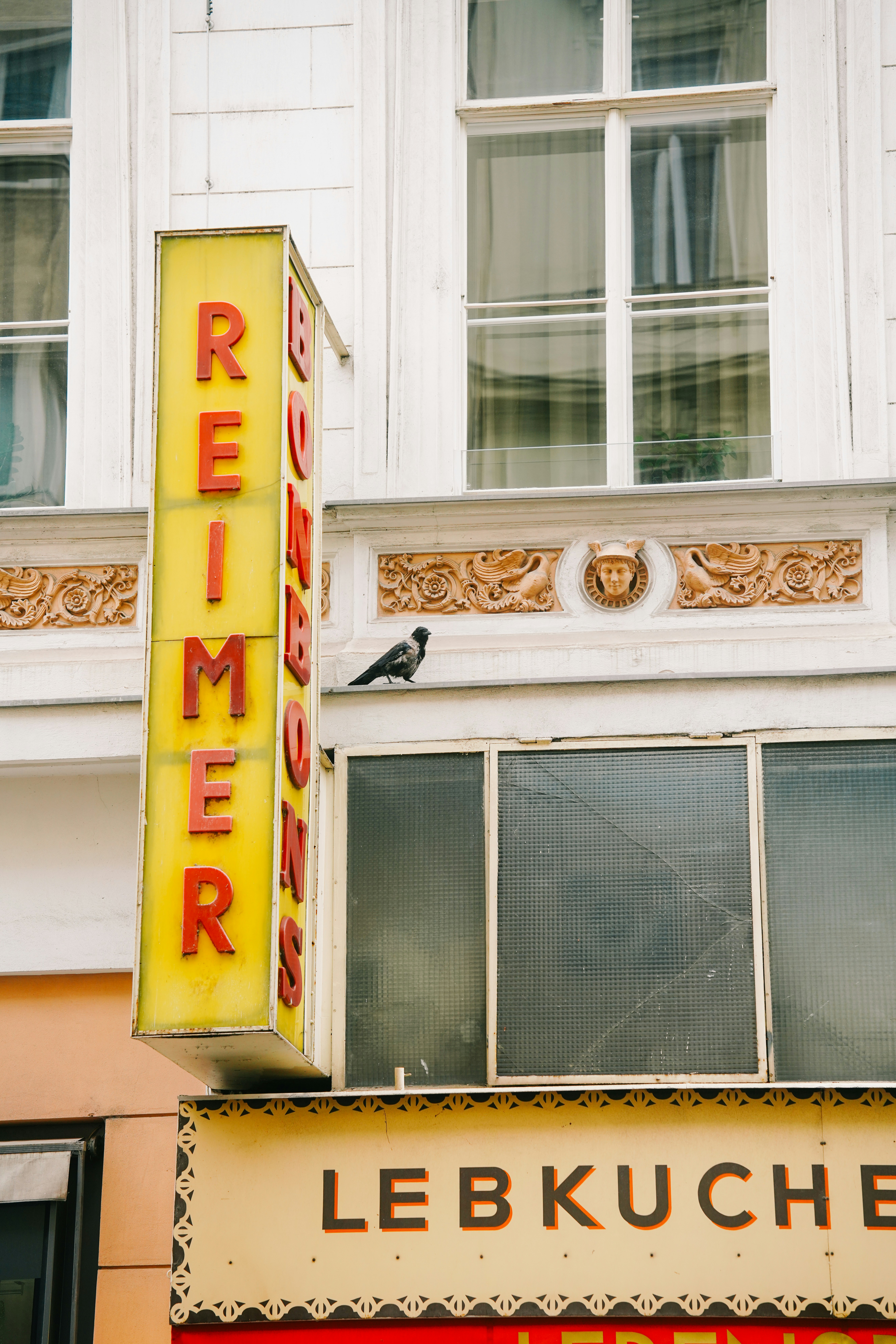 Retro Yellow REIMER Signage Framing an Ornate Lebkuchen Storefront with a Pigeon on the Ledge
