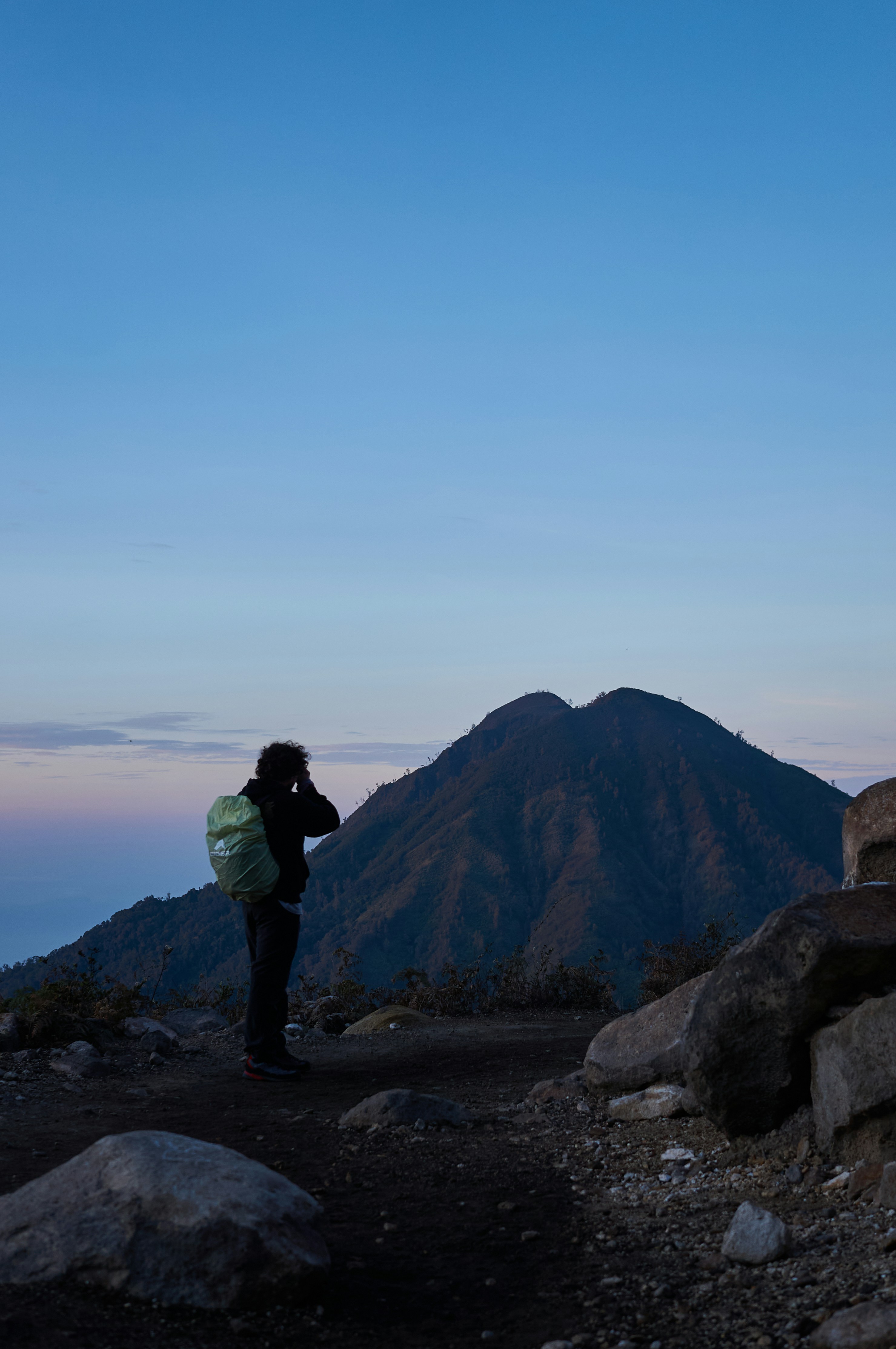 Blue-hour silhouette on the ridge: a lone hiker gazes toward the sea-mountain horizon