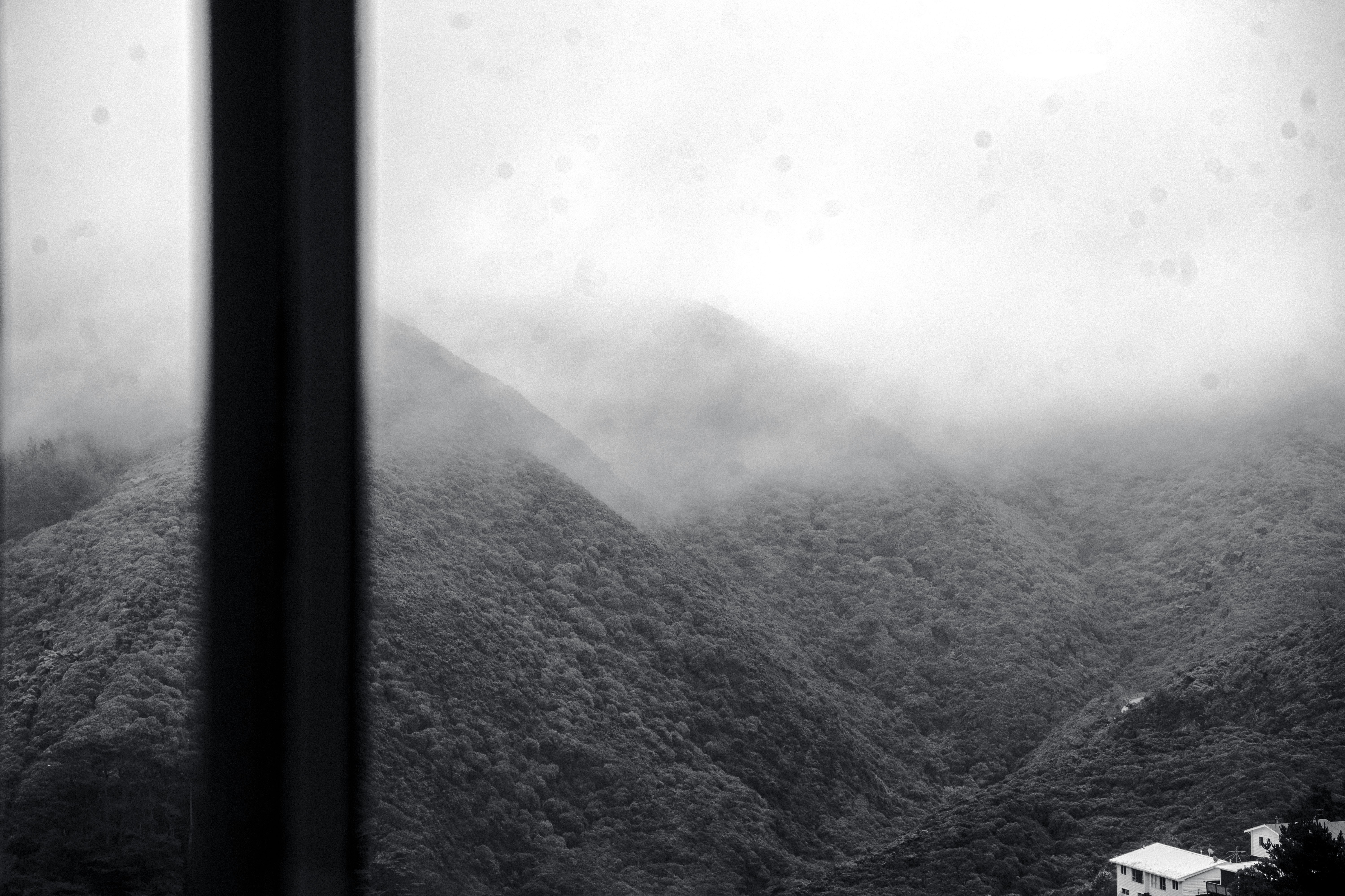 Fog drapes over lush, mountainous terrain with a house nestled in the foreground.