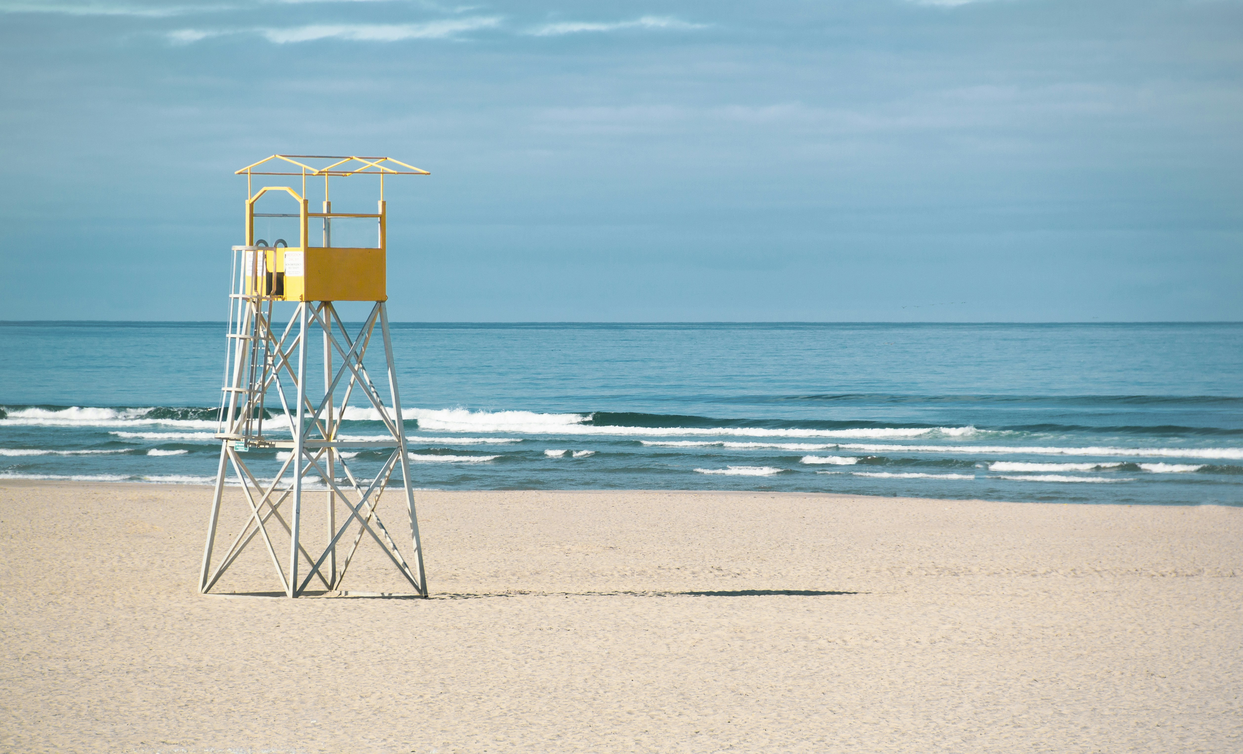 Yellow lifeguard tower stands on a sandy beach with gentle waves in the background.