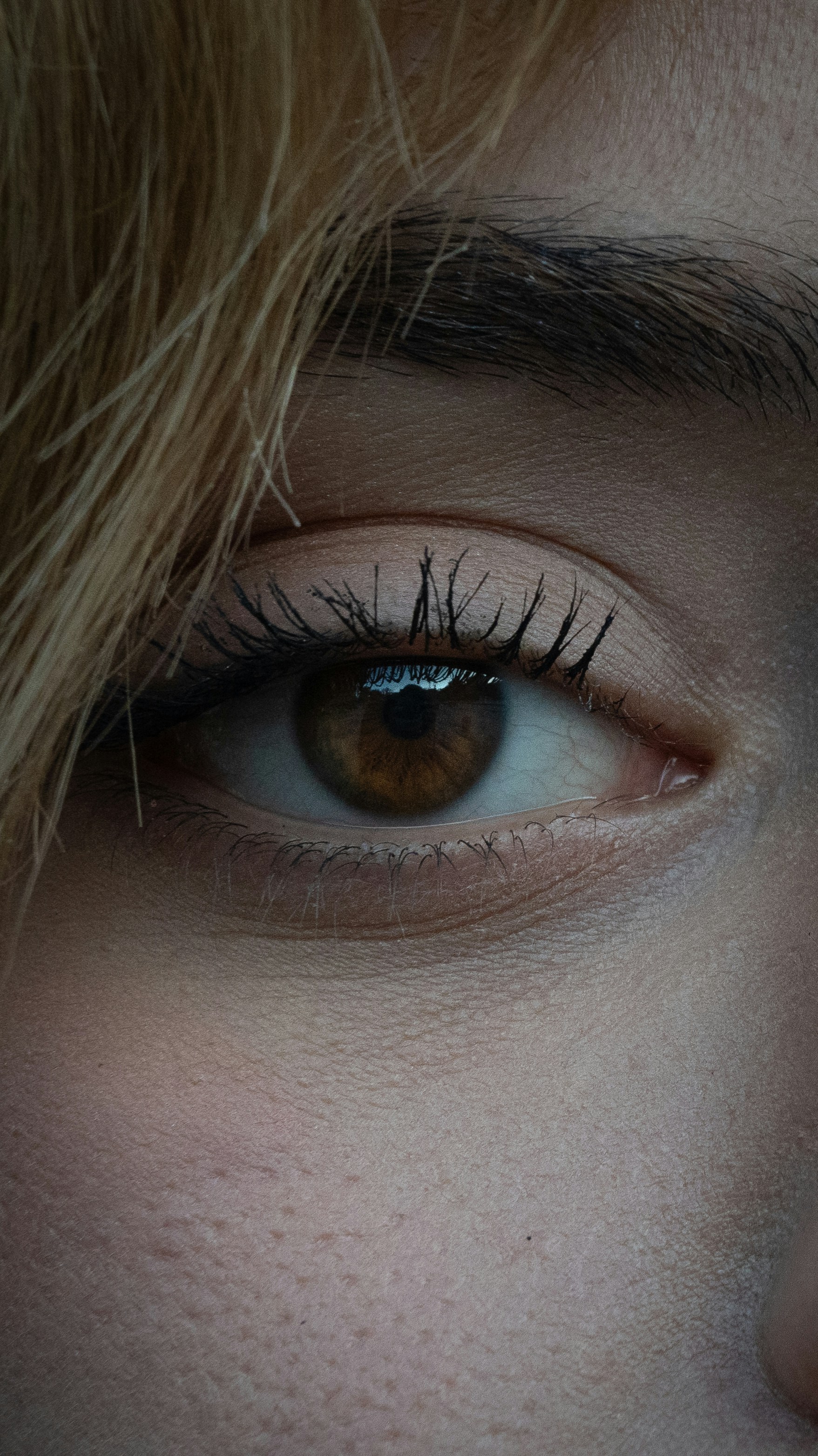 Close-up of a human eye, showcasing intricate details of the iris and eyelashes, framed by soft blonde hair. The image captures a moment of contemplation.