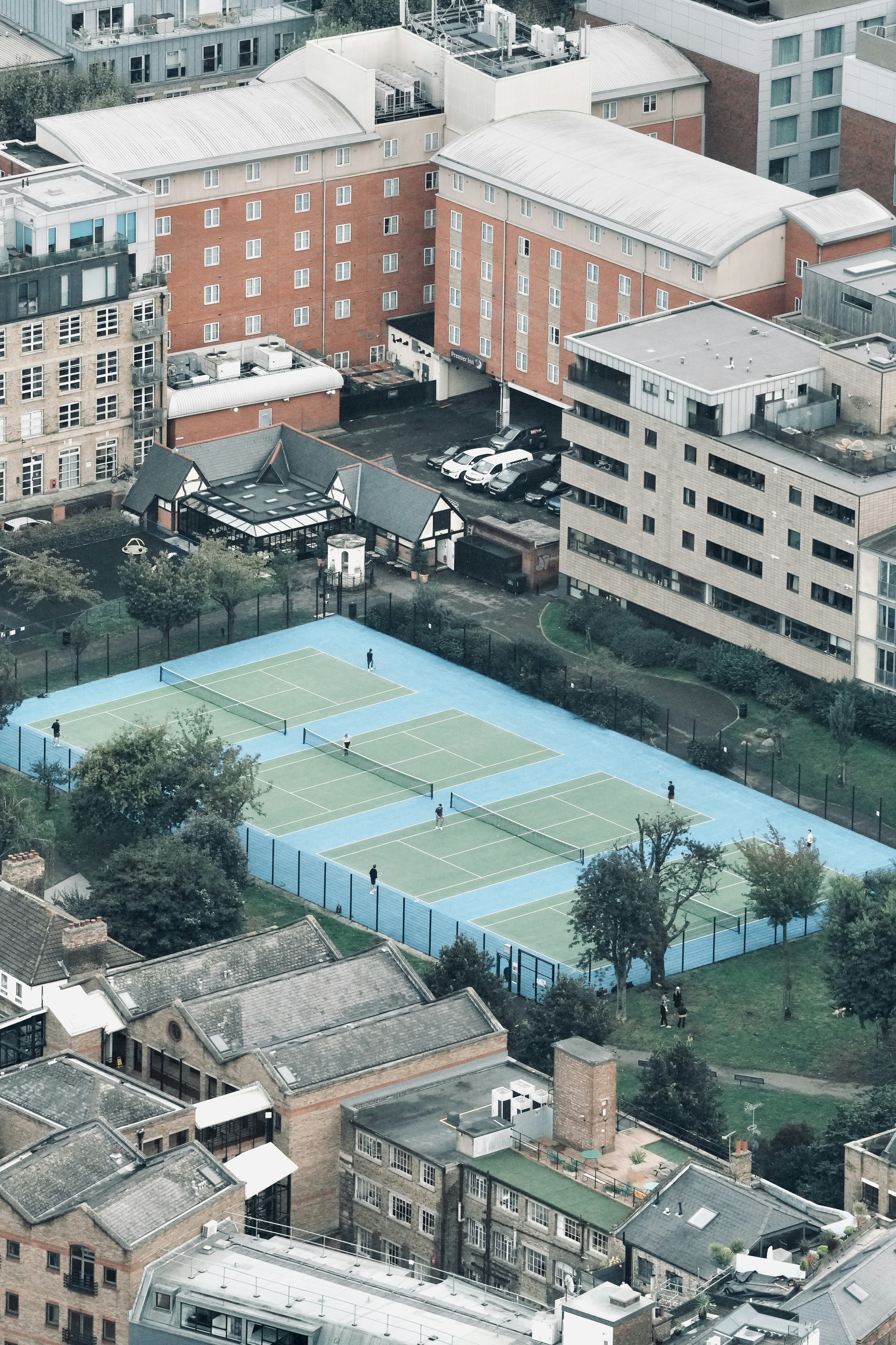 Blue Courts below a Brickwork Skyline: An Aerial Campus Tennis Scene