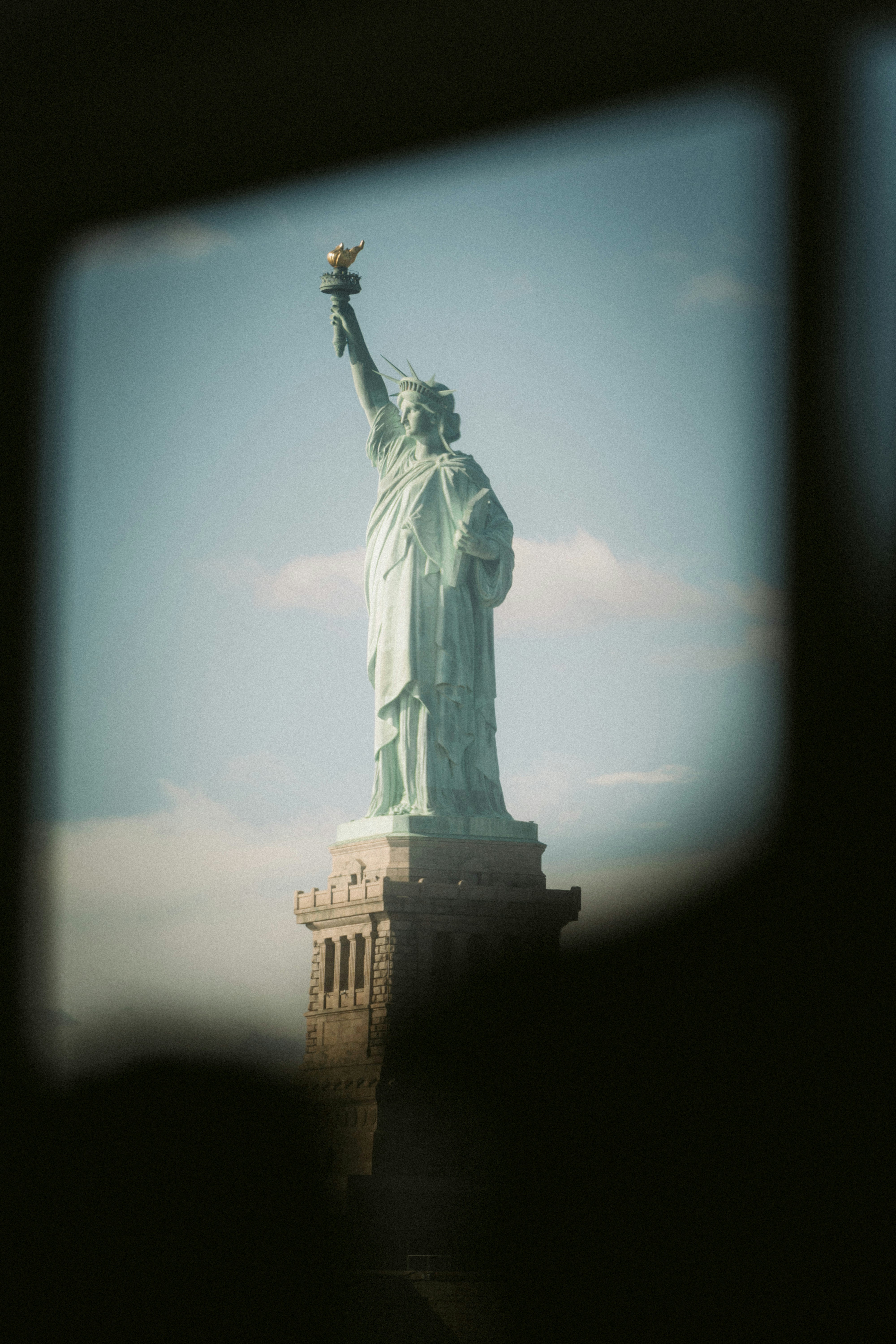 Statue of Liberty framed through a window, showcasing its majestic presence against a clear sky.