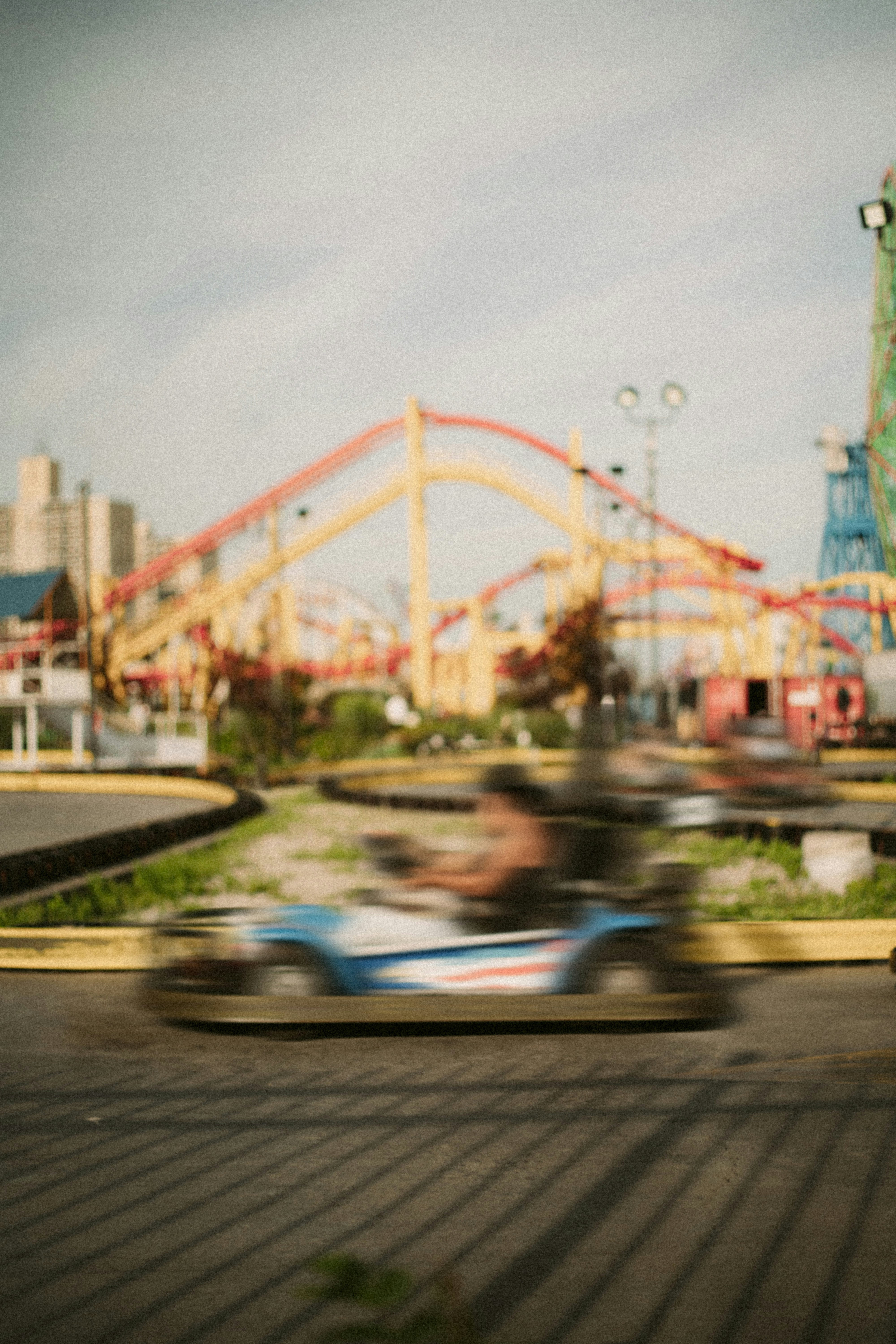 Rainbow Rails in Motion: Blurred Go-Kart Sprint Under the Park's Roller Coaster