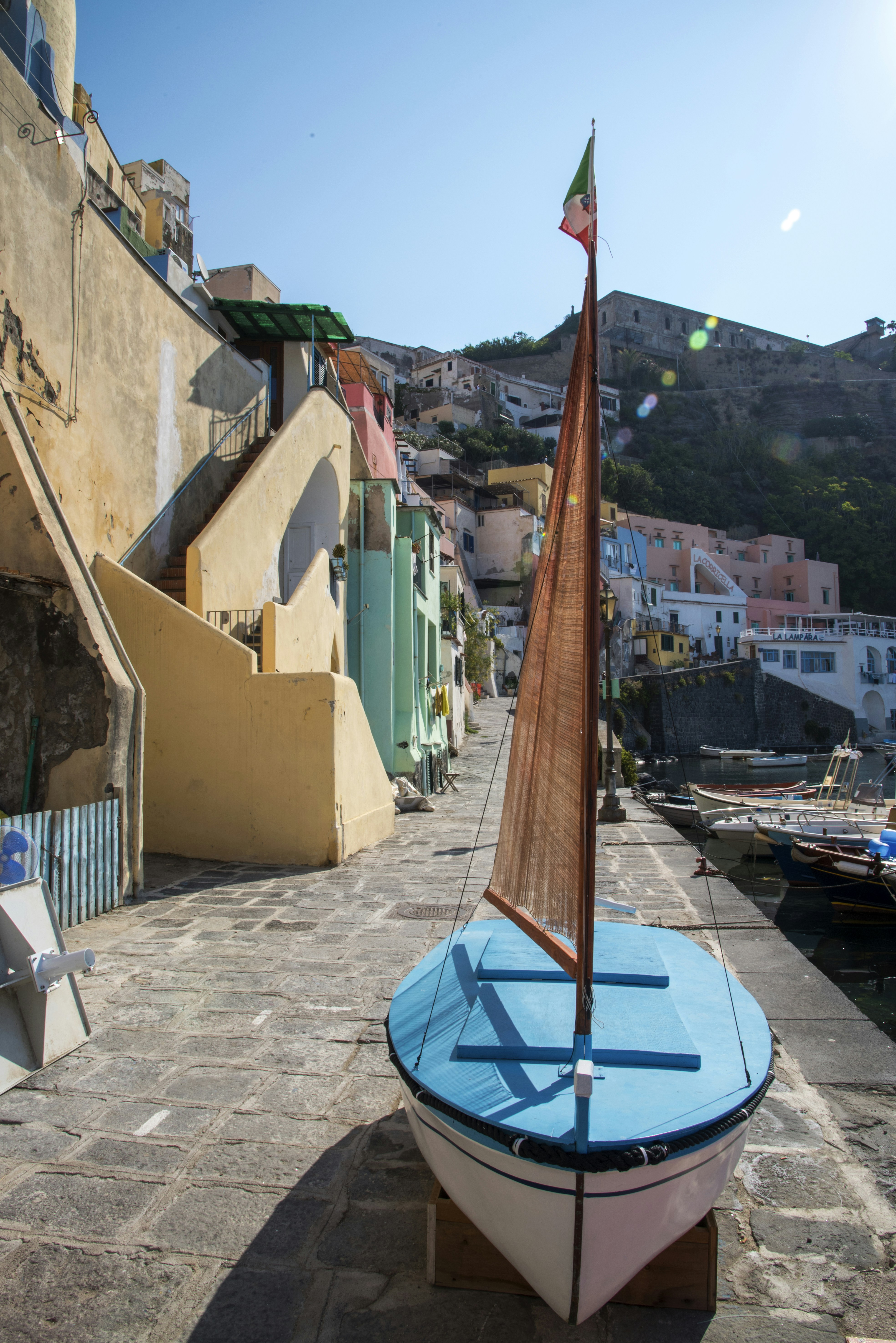 Blue-Deck Sailboat Resting Among Sunlit Pastel Alleys by the Harbor