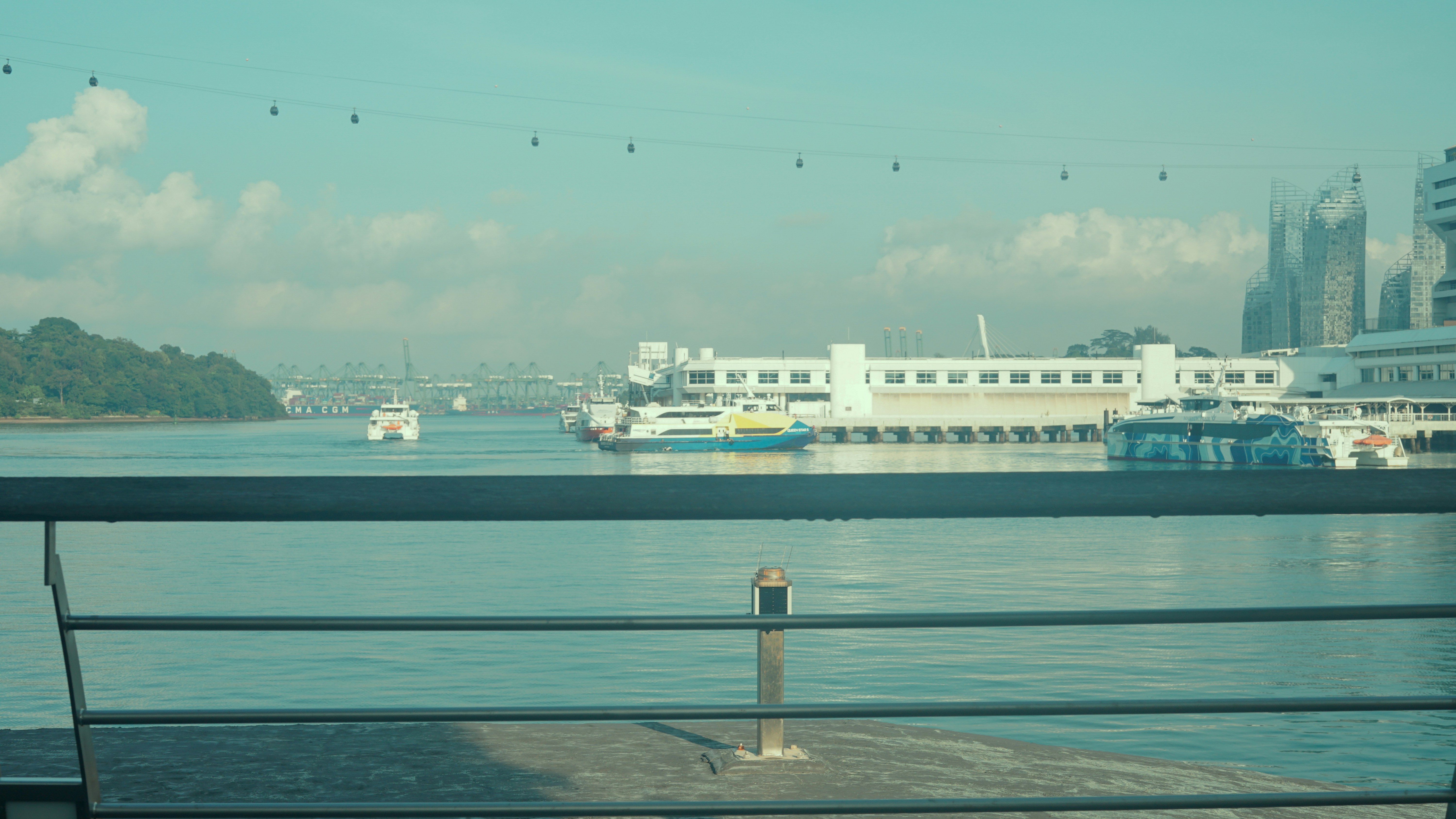 Boats docked at a waterfront harbor with a backdrop of modern buildings and a clear sky. The scene captures the blend of nature and urban life.