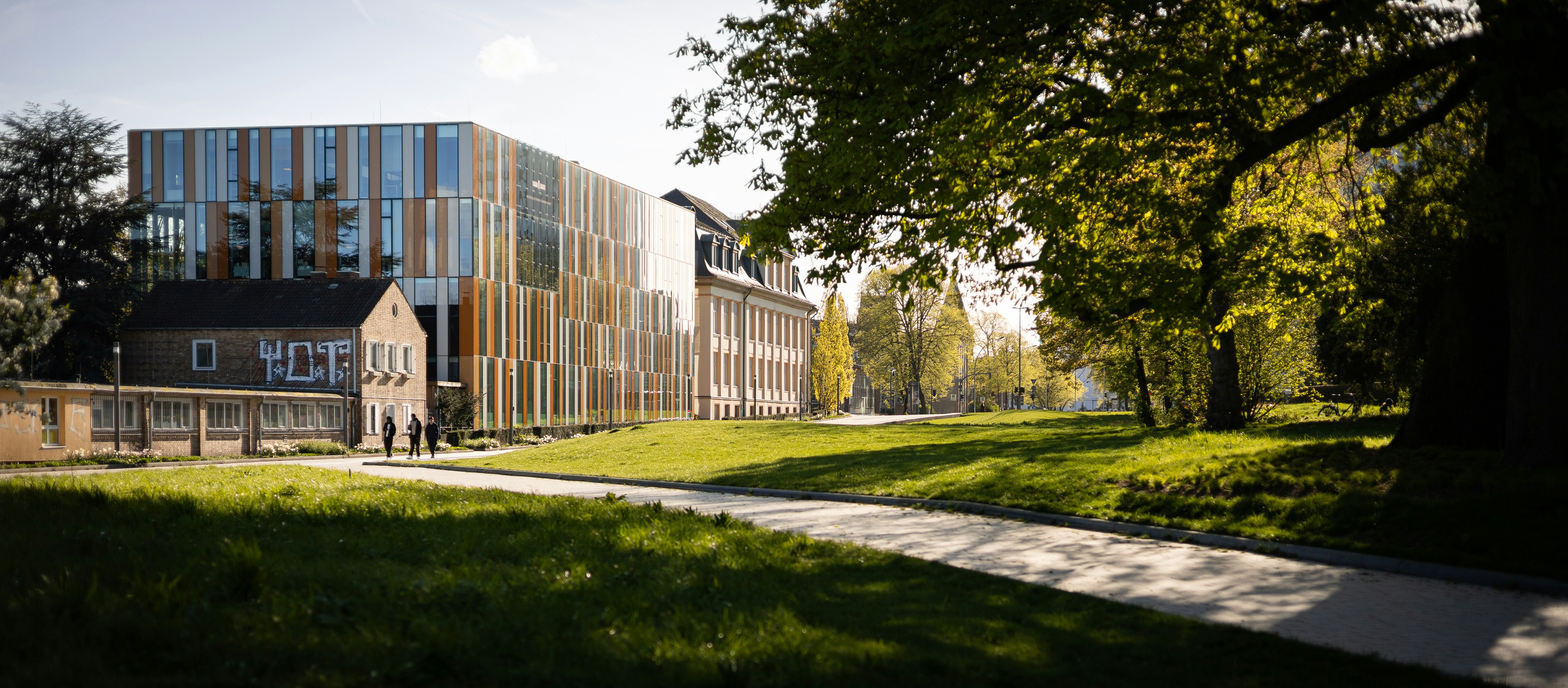 A modern university building with a traditional building in the background, surrounded by a green park. | A large building sitting on top of a lush green field