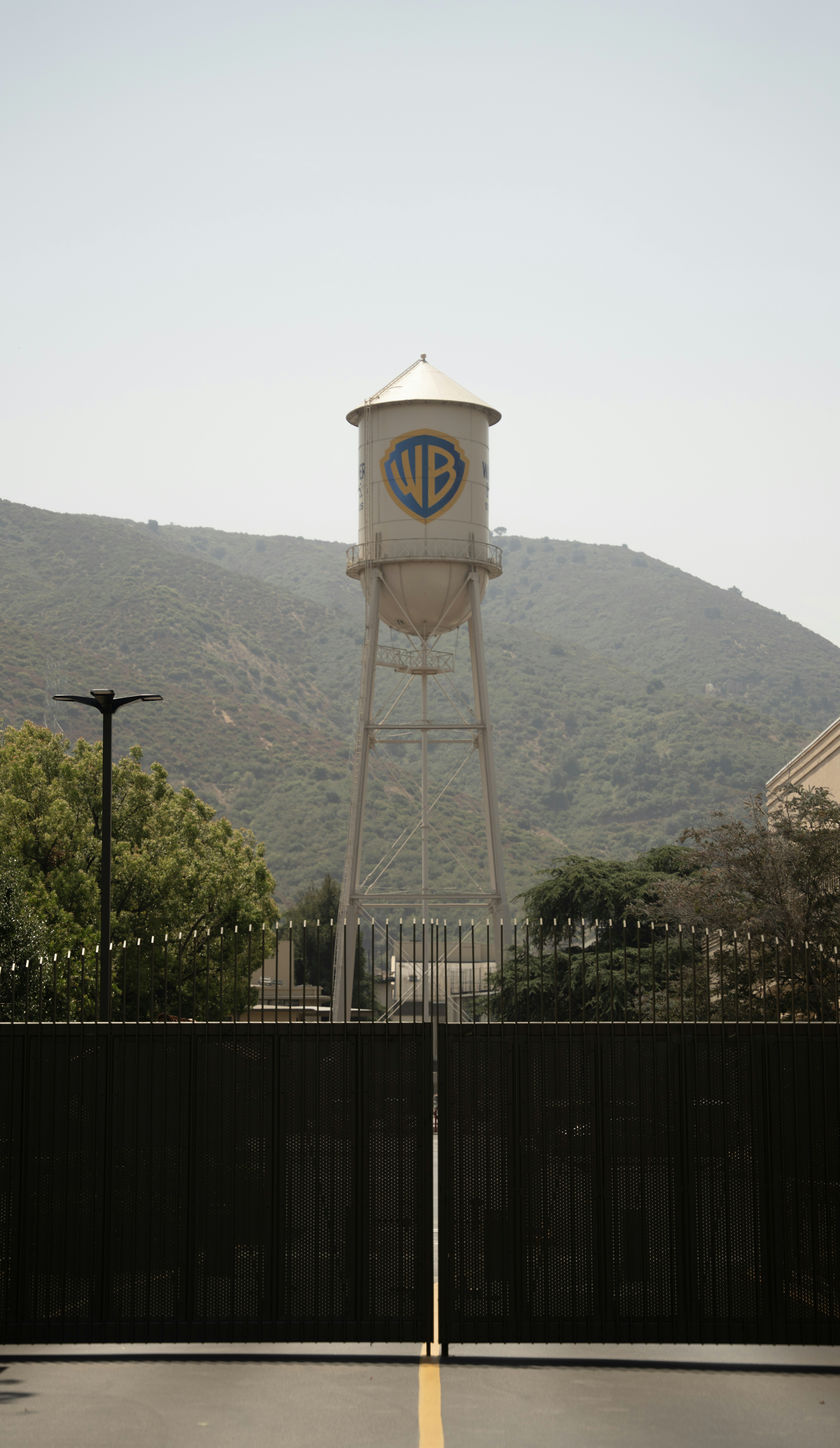 Water tower with WB logo stands tall against green hills and clear sky.