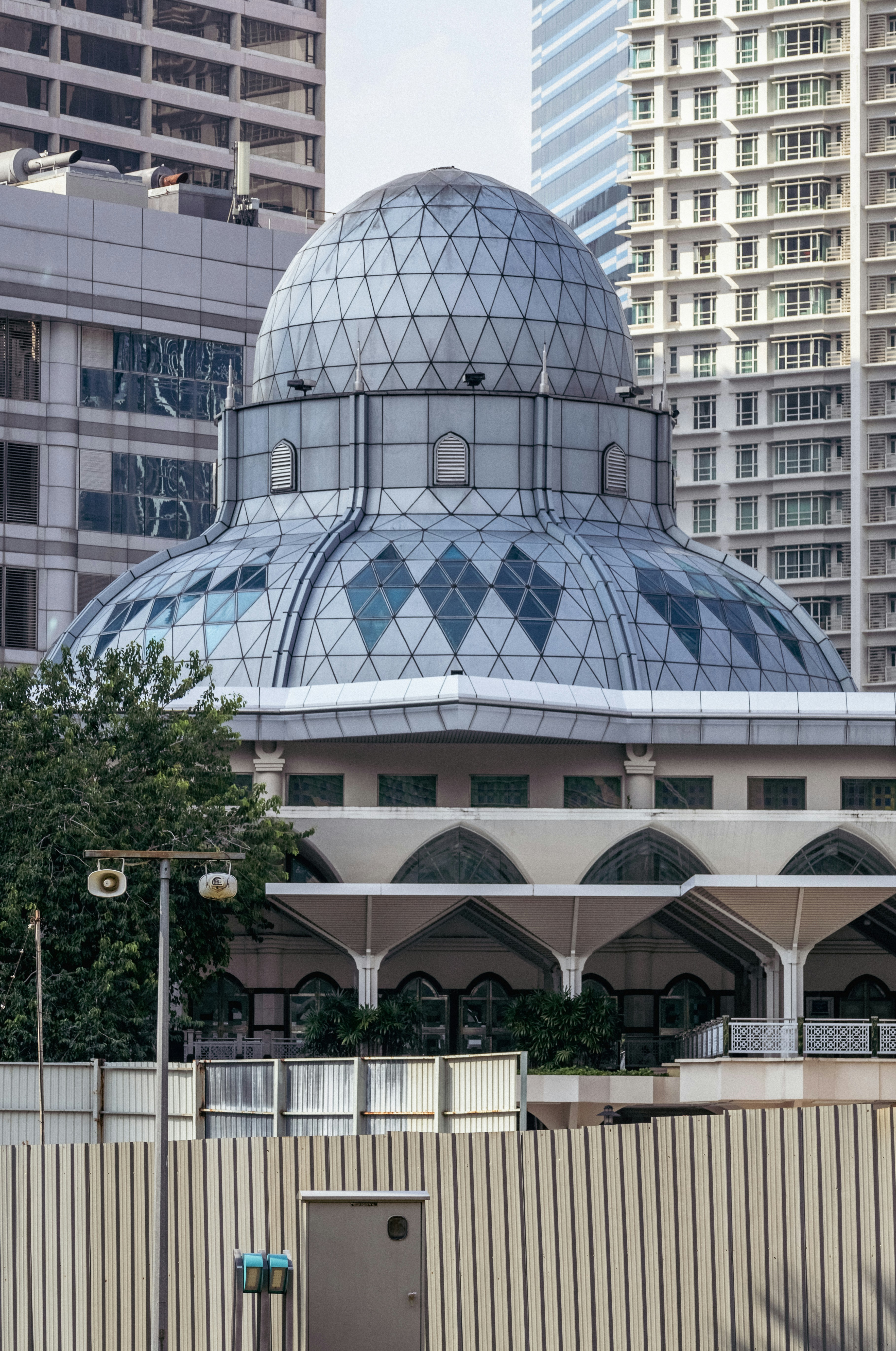 A modern mosque with a distinctive glass dome surrounded by urban architecture, showcasing the blend of spirituality and contemporary design.