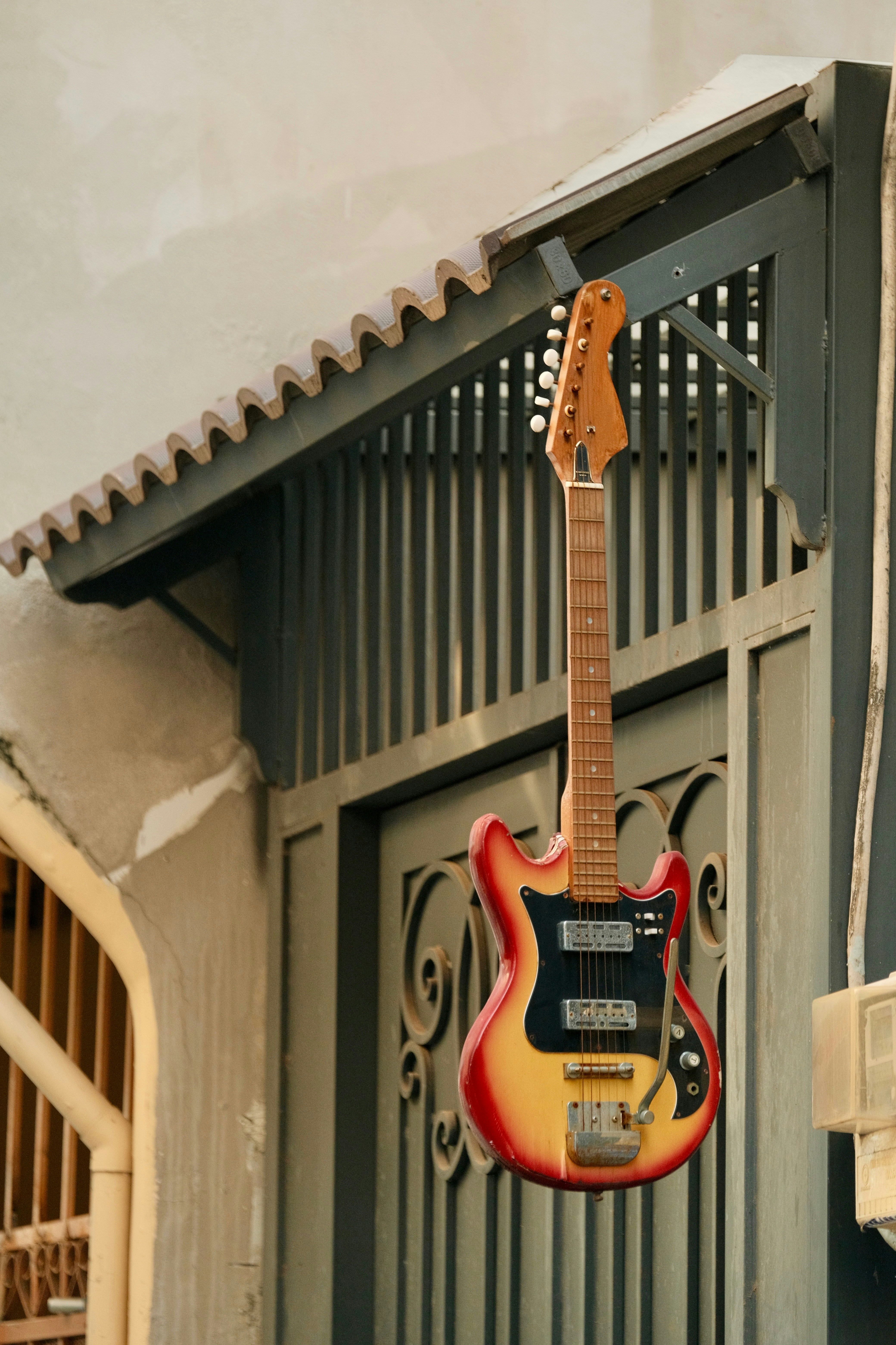 Sunburst Electric Guitar Hangs on a Weathered Gate Under a Tiled Awning