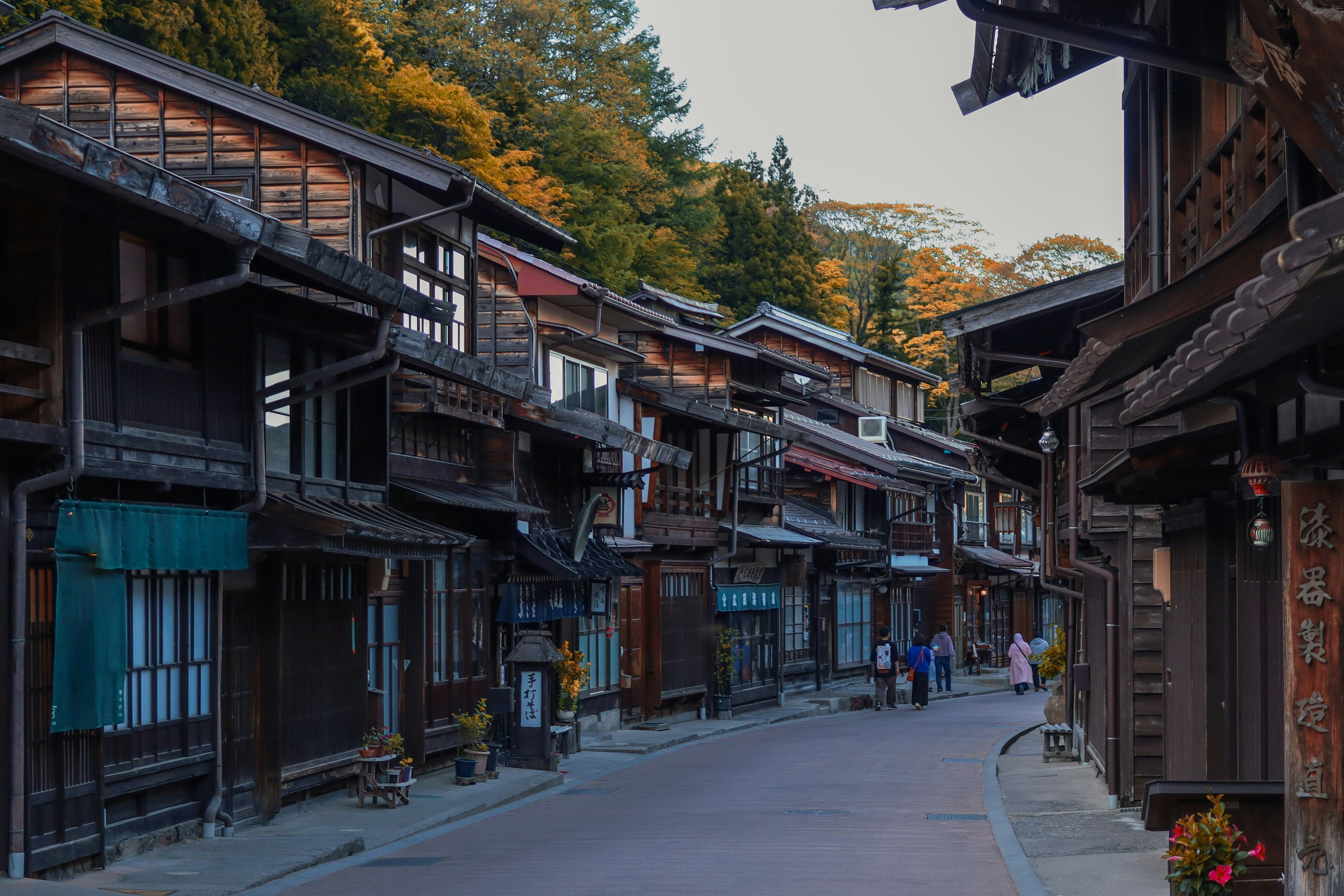 Historic street in Narai-juku lined with traditional wooden buildings under a canopy of autumn leaves.