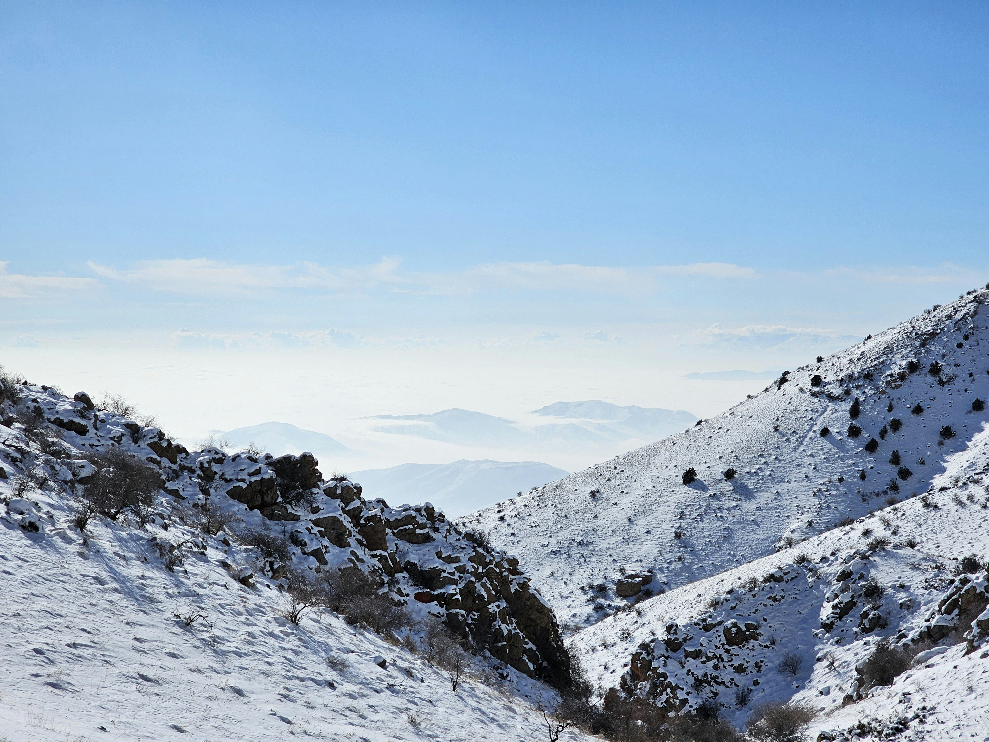 Snow-covered mountain slopes reveal a serene landscape under a clear blue sky, with distant peaks fading into the horizon.