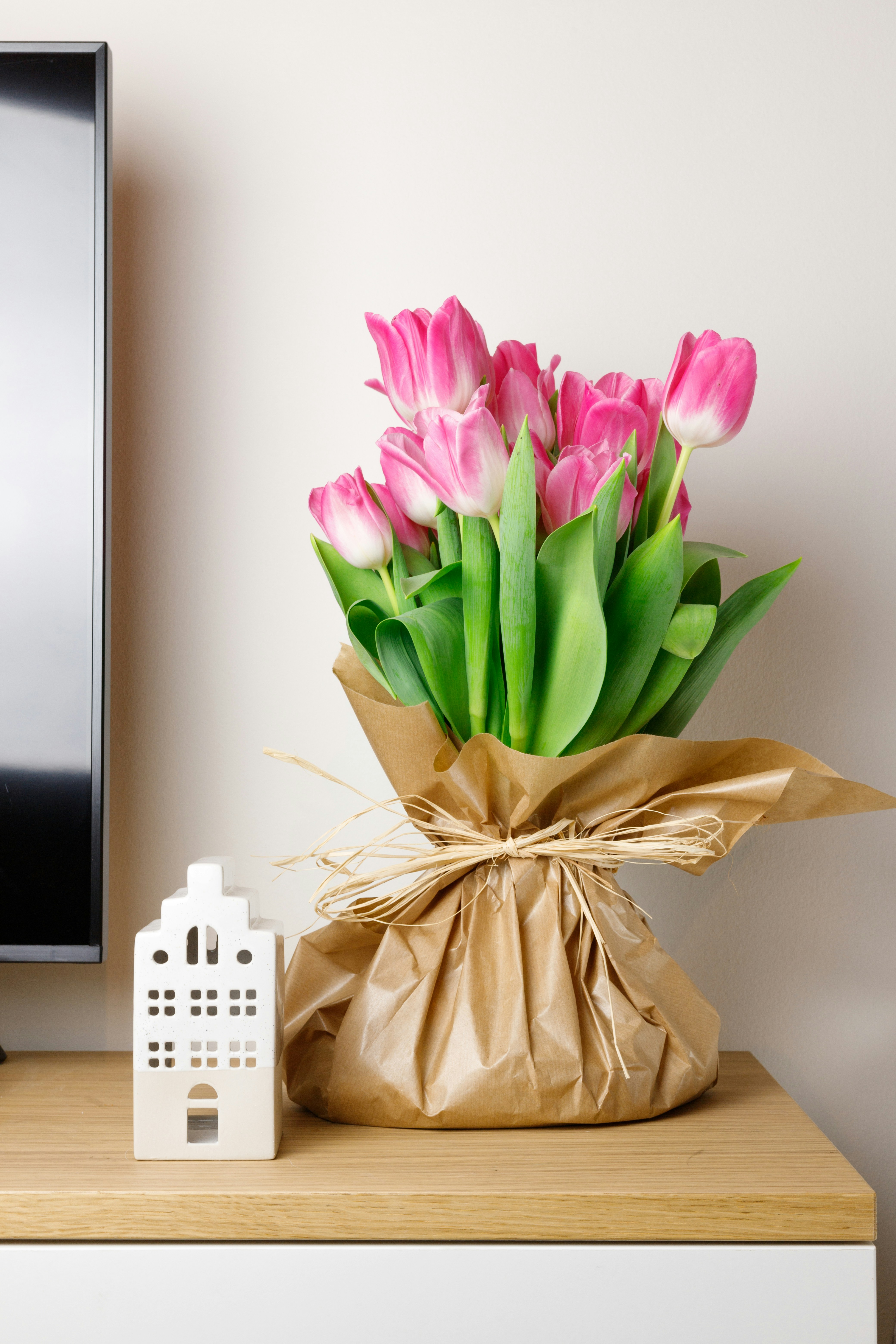 A bouquet of pink tulips sitting on a desk next to a computer monitor ...