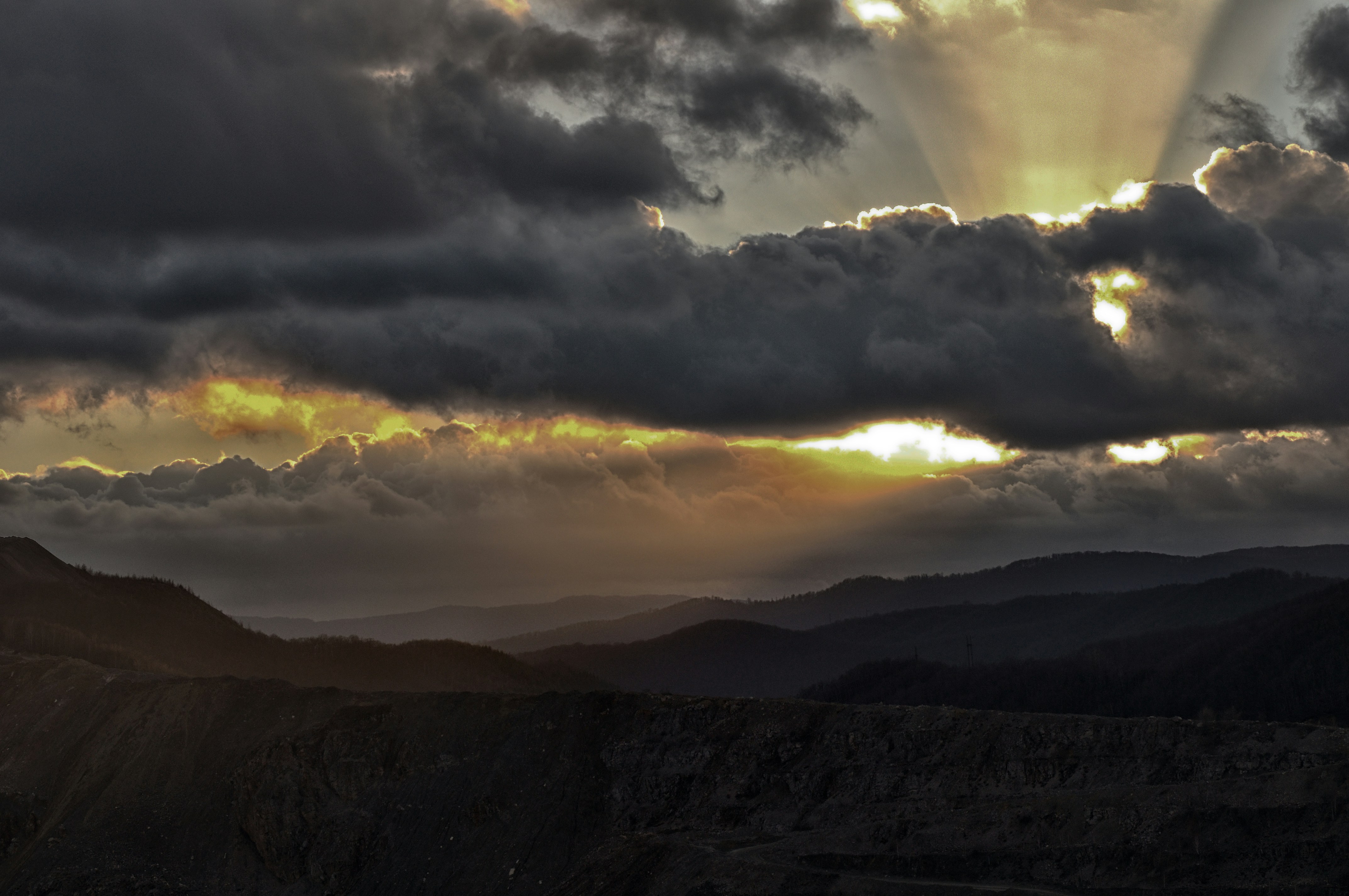 Sunset light piercing through thick clouds over mountainous terrain.