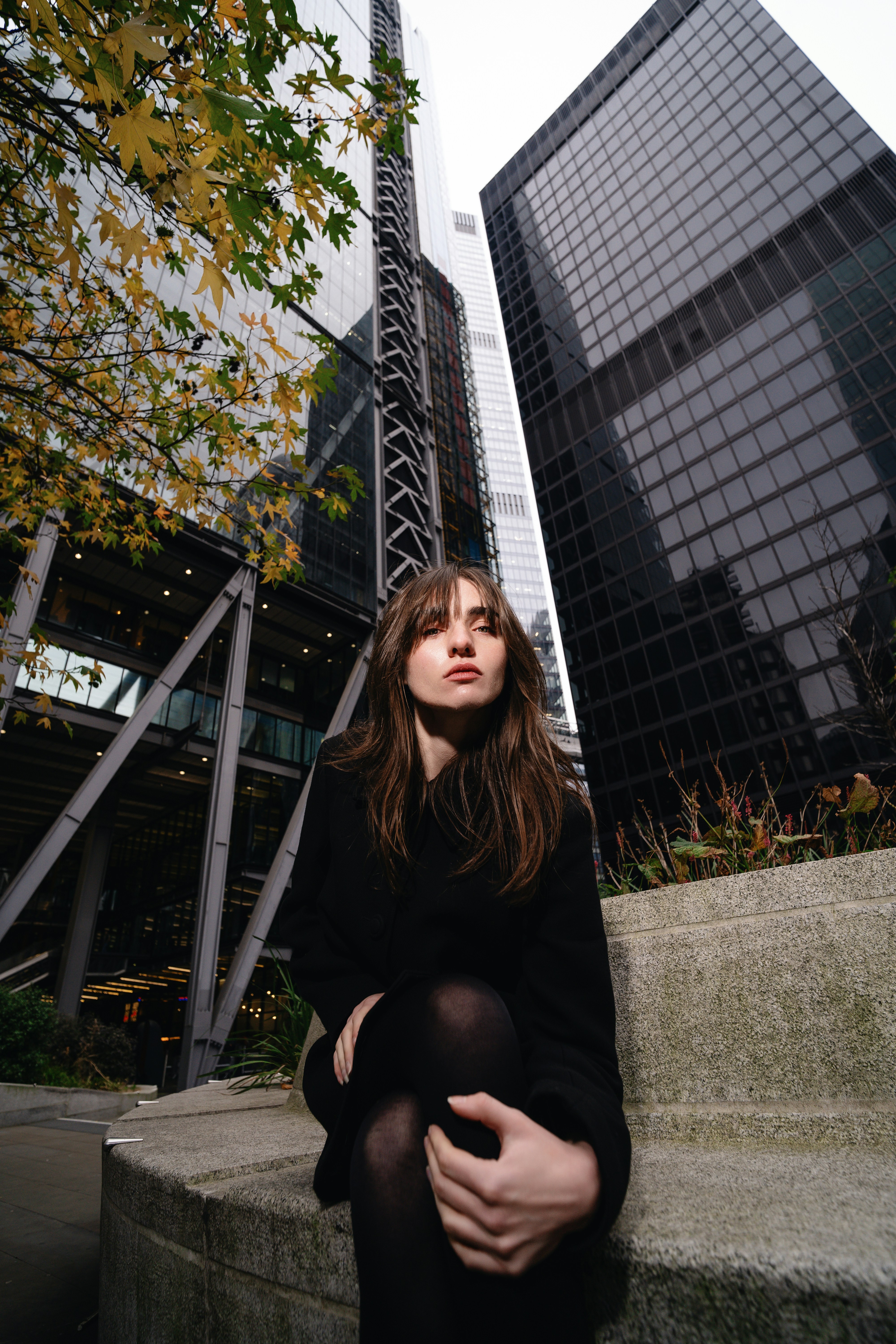 A woman sitting on a ledge in front of tall buildings photo – Free ...