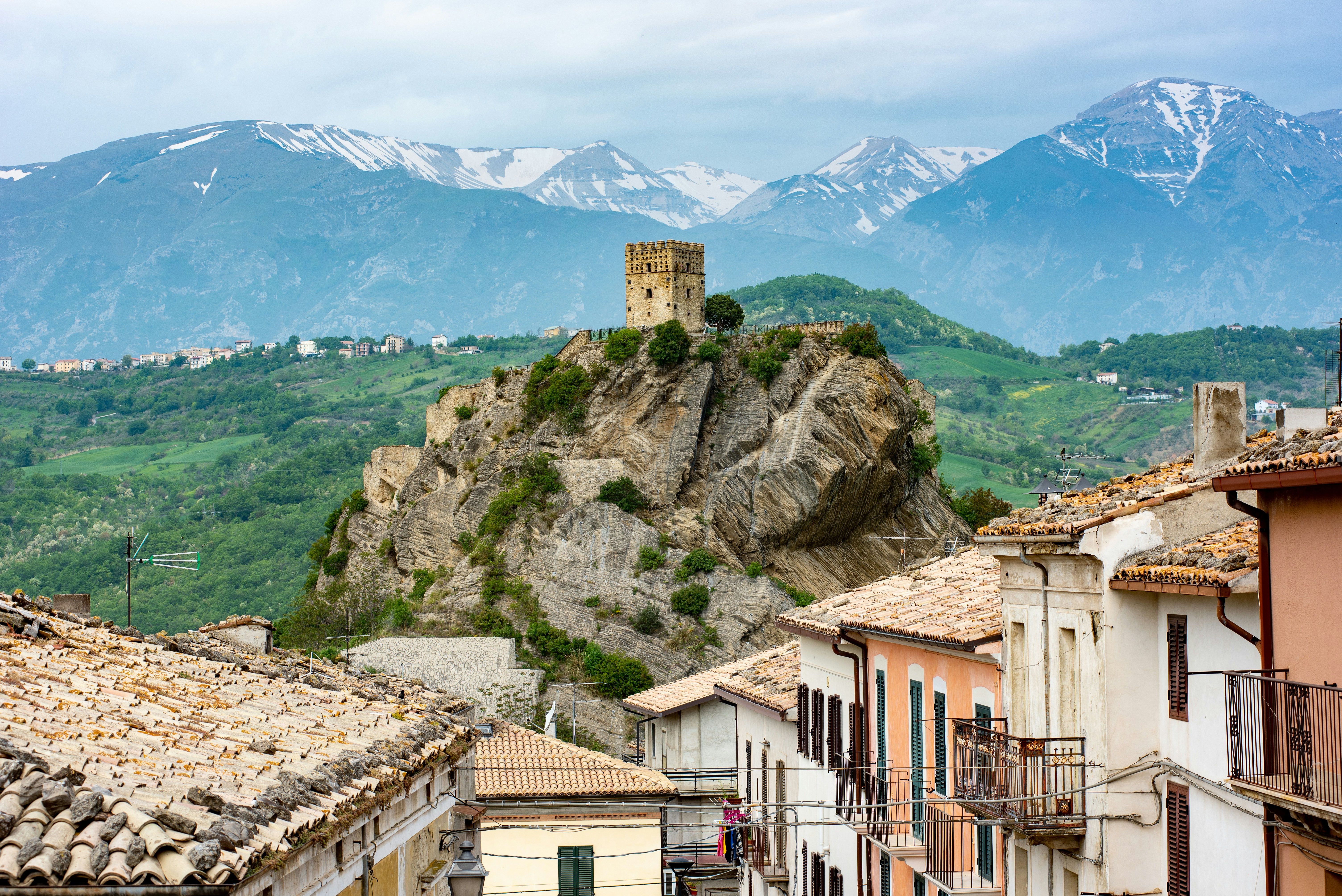 Ancient stone castle perched on a rocky hilltop with snow-capped mountains in the background.