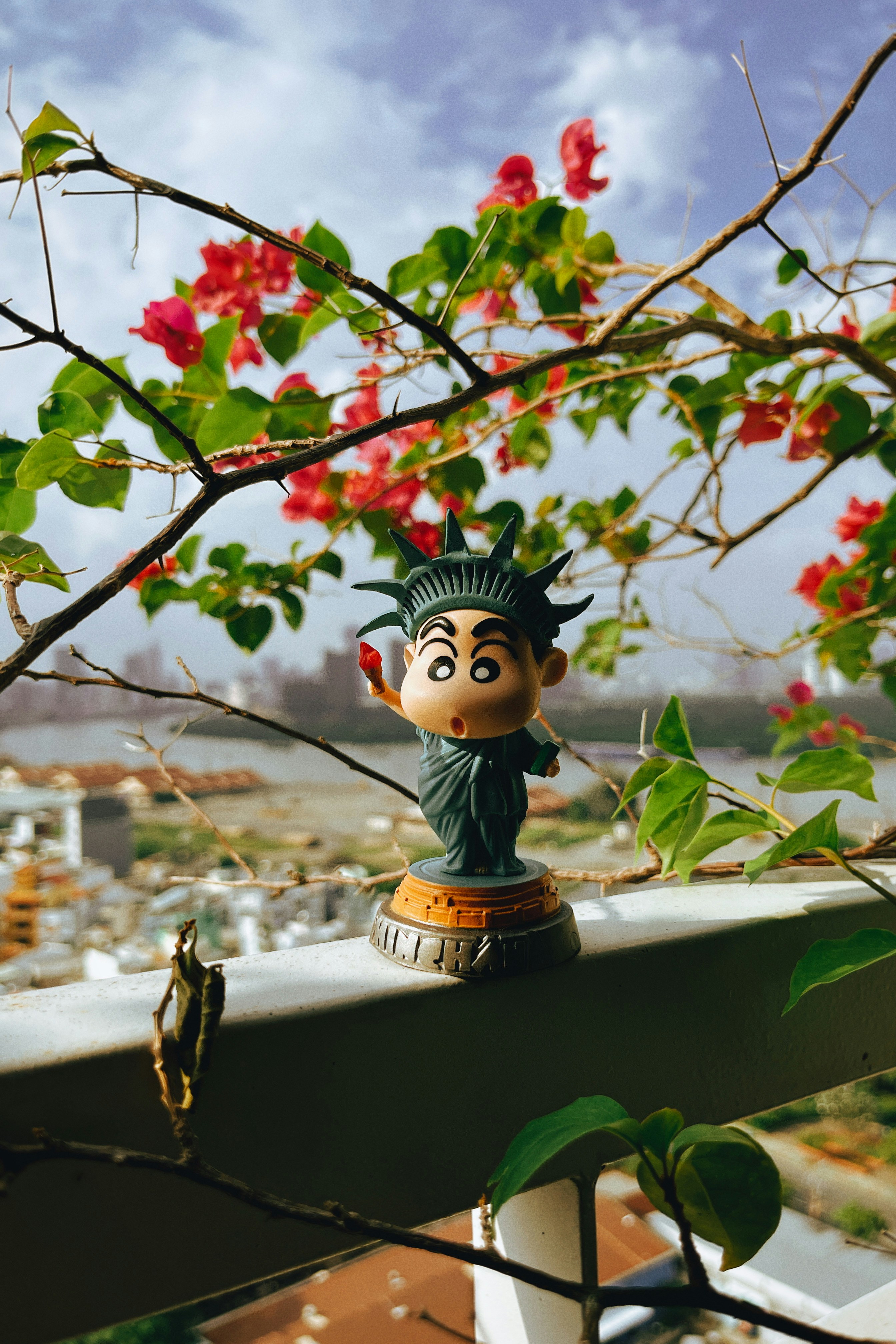 Tiny Liberty Guarded by Spring Blooms on a City Balcony