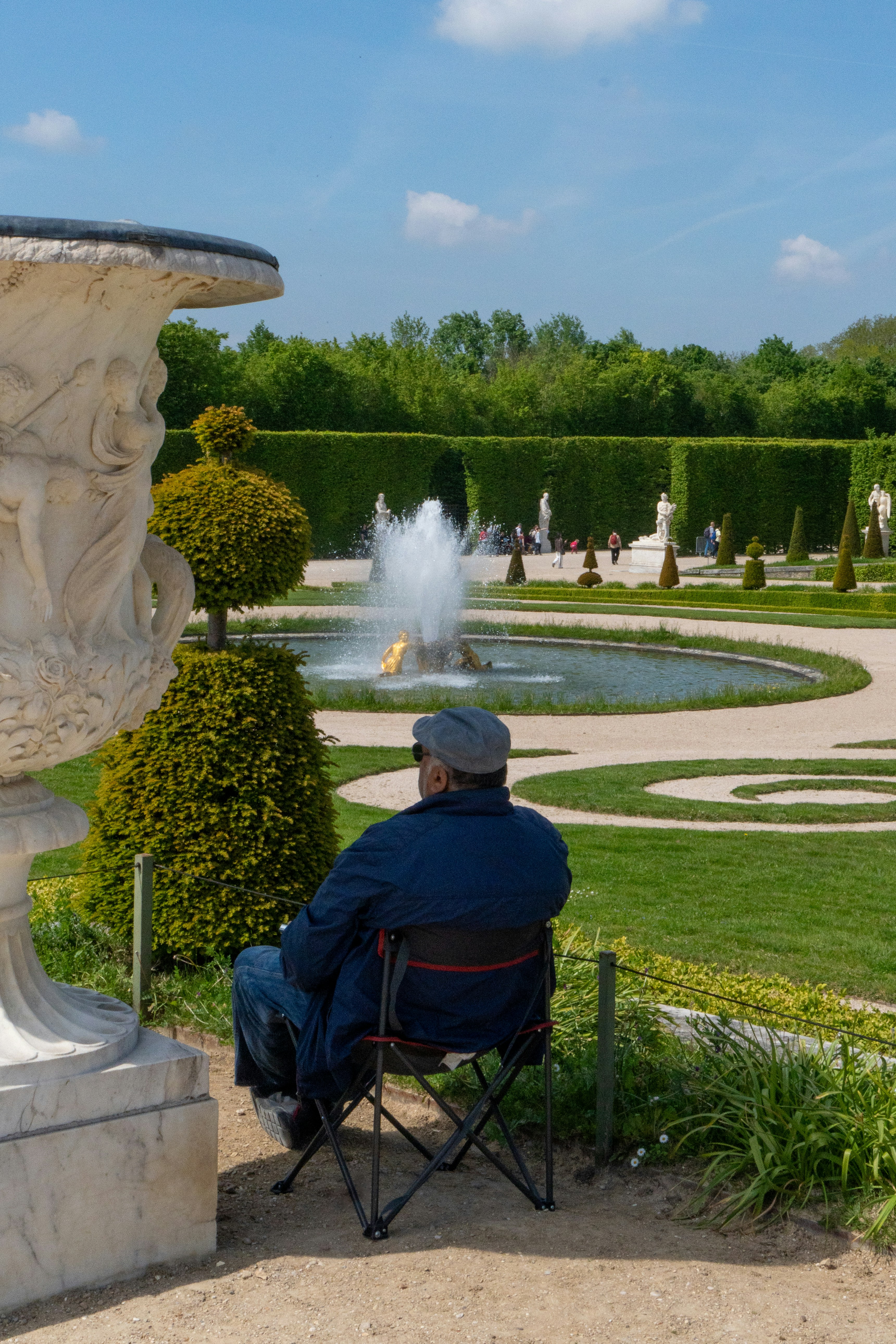 Quiet Moment by the Fountain: Man in a Blue Jacket in a Formal Garden