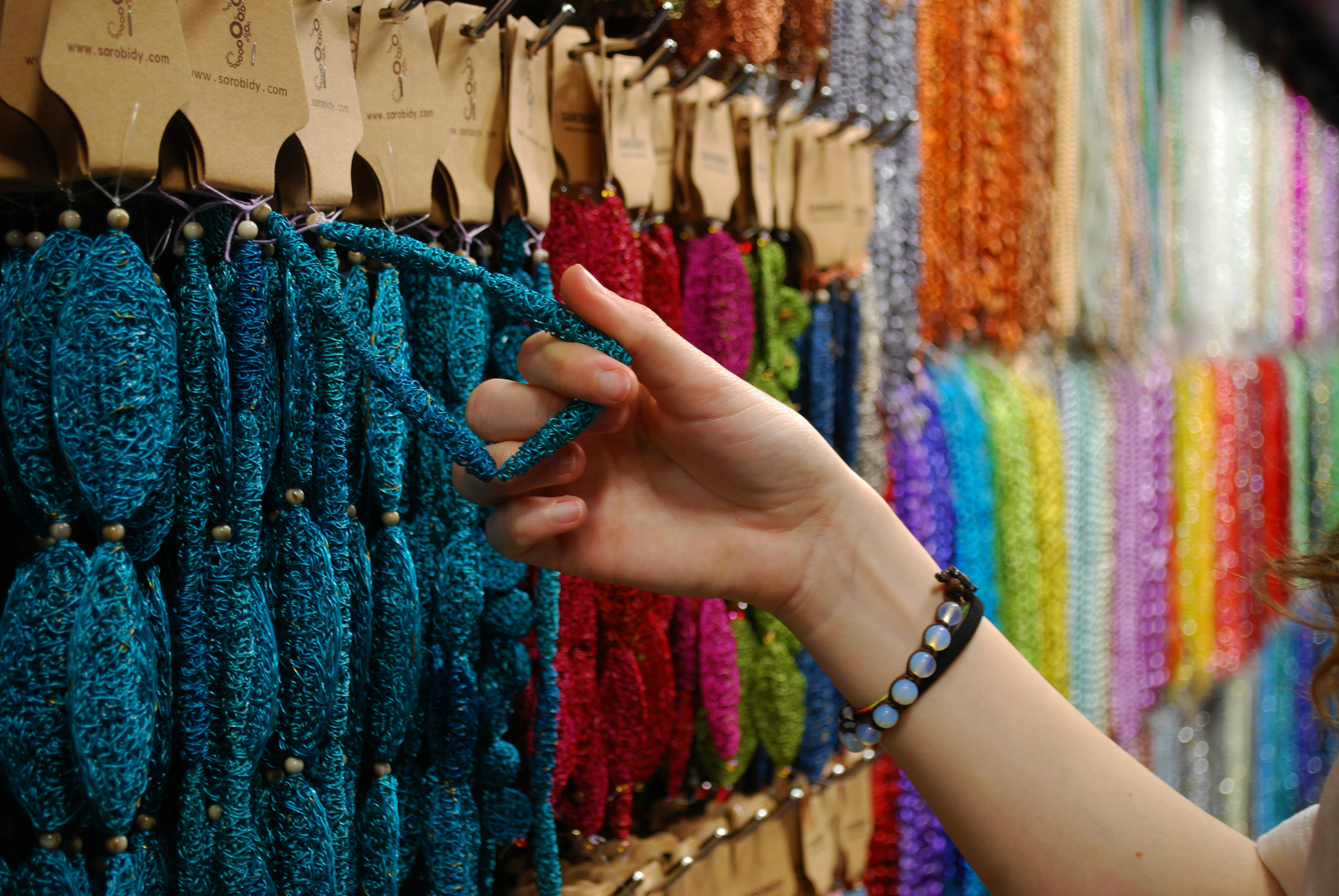 Palette of Tassels: A Hand Reaches for Blue Velvet in a Rainbow Yarn Display