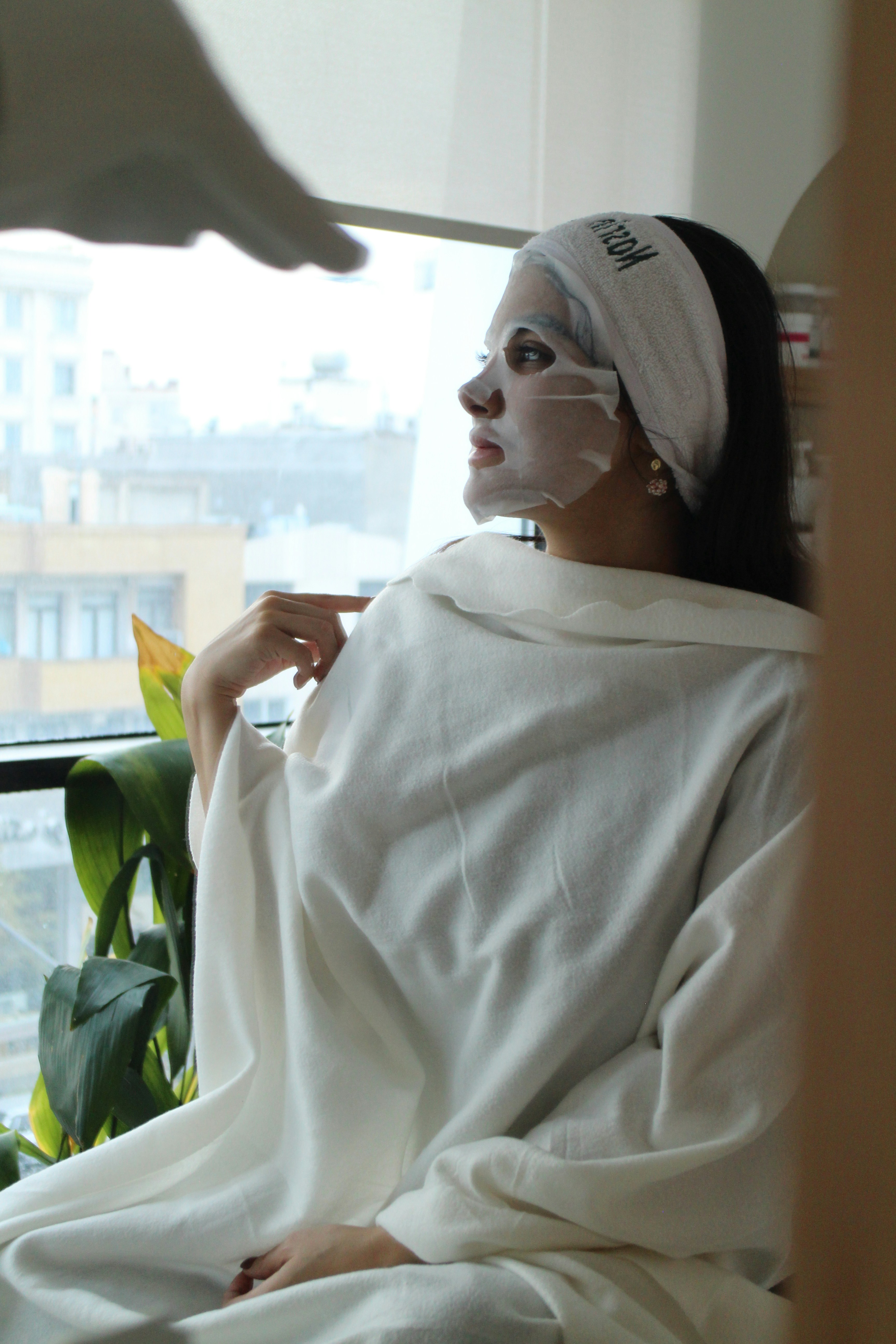 Portrait in White: A Quiet Moment with a Facial Mask by the Window