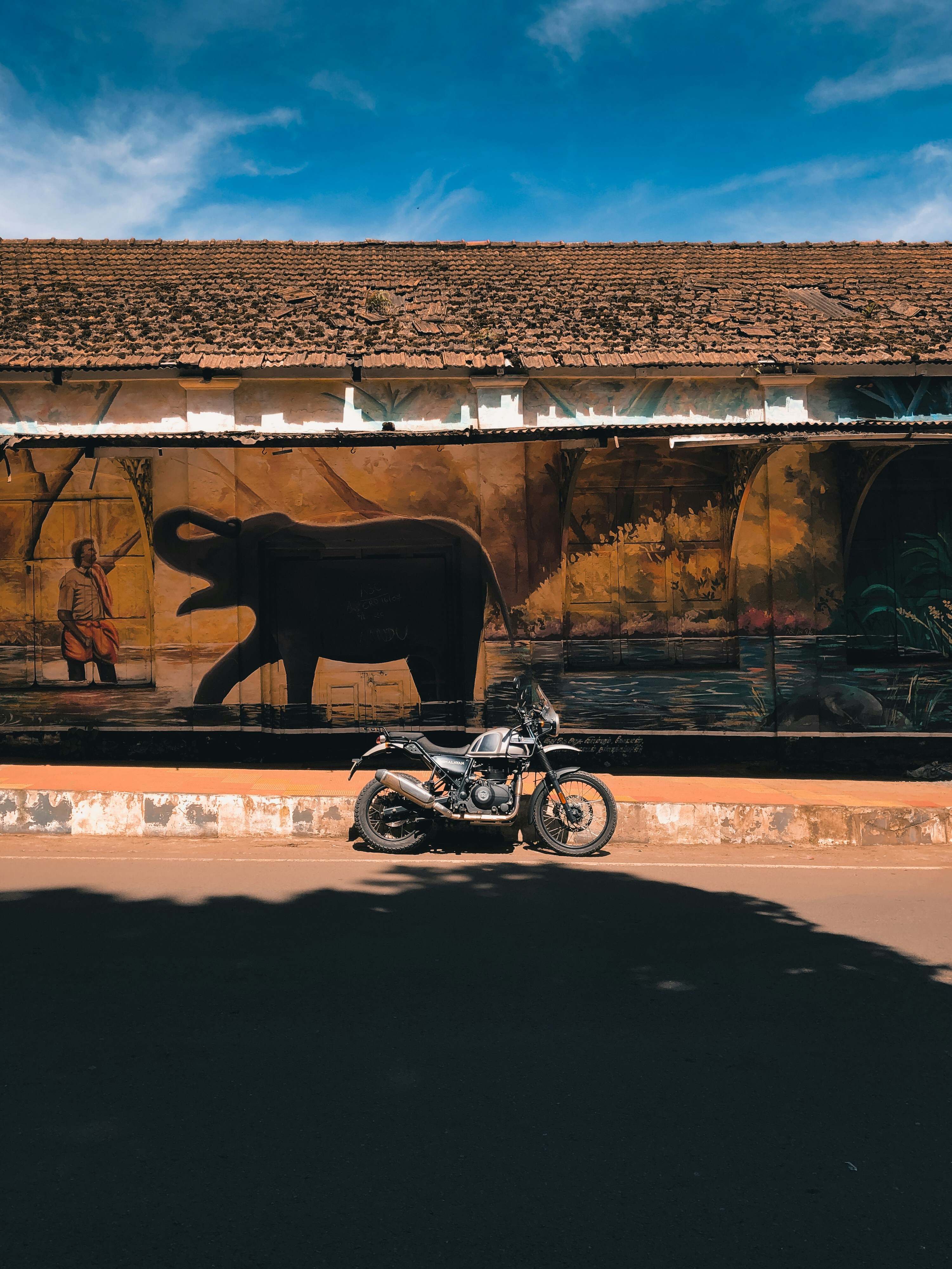 Moto Under a Colorful Elephant Mural on a Sunlit Street