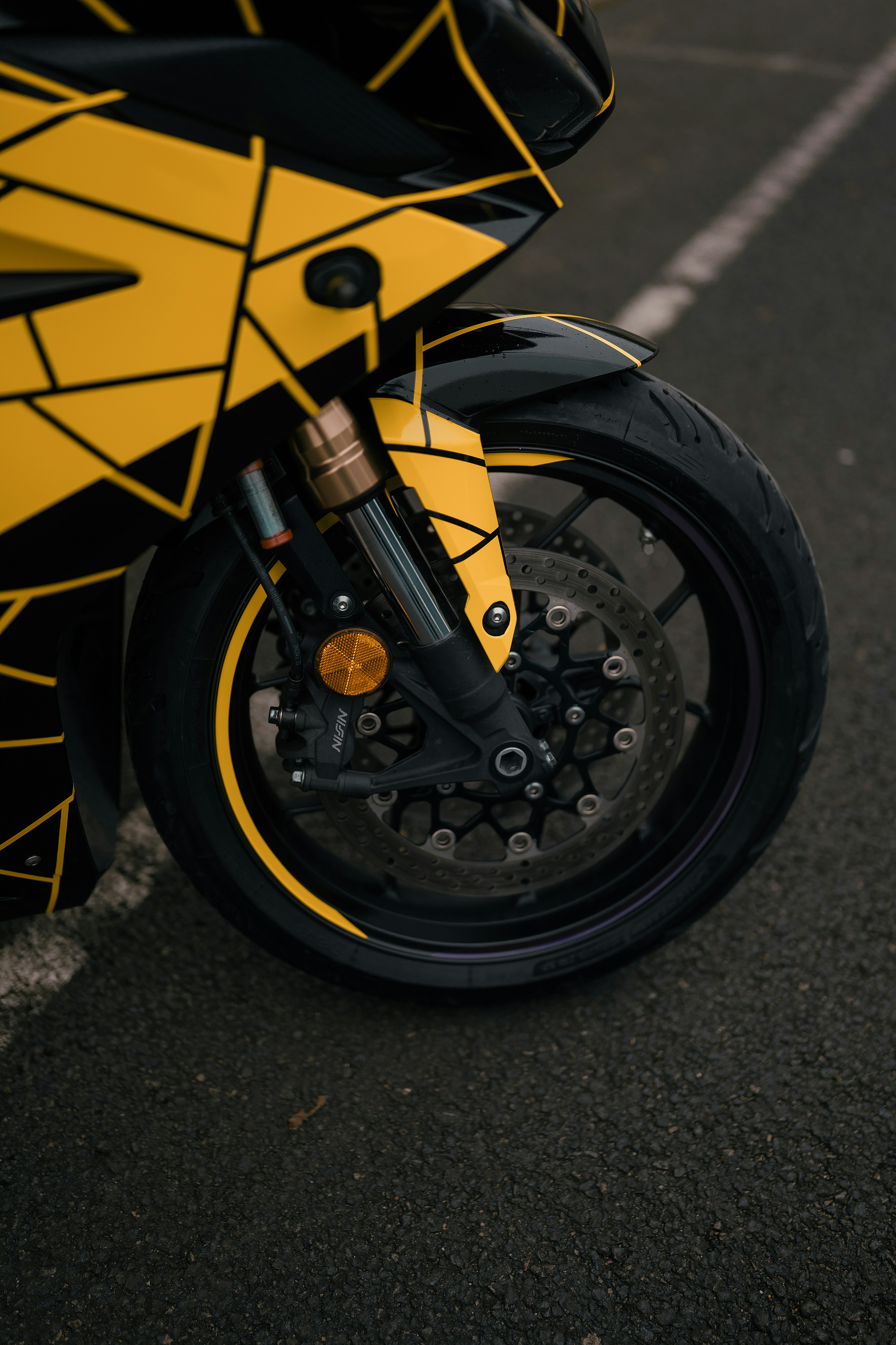 Motorcycle wheel with bold yellow and black geometric pattern against dark asphalt.