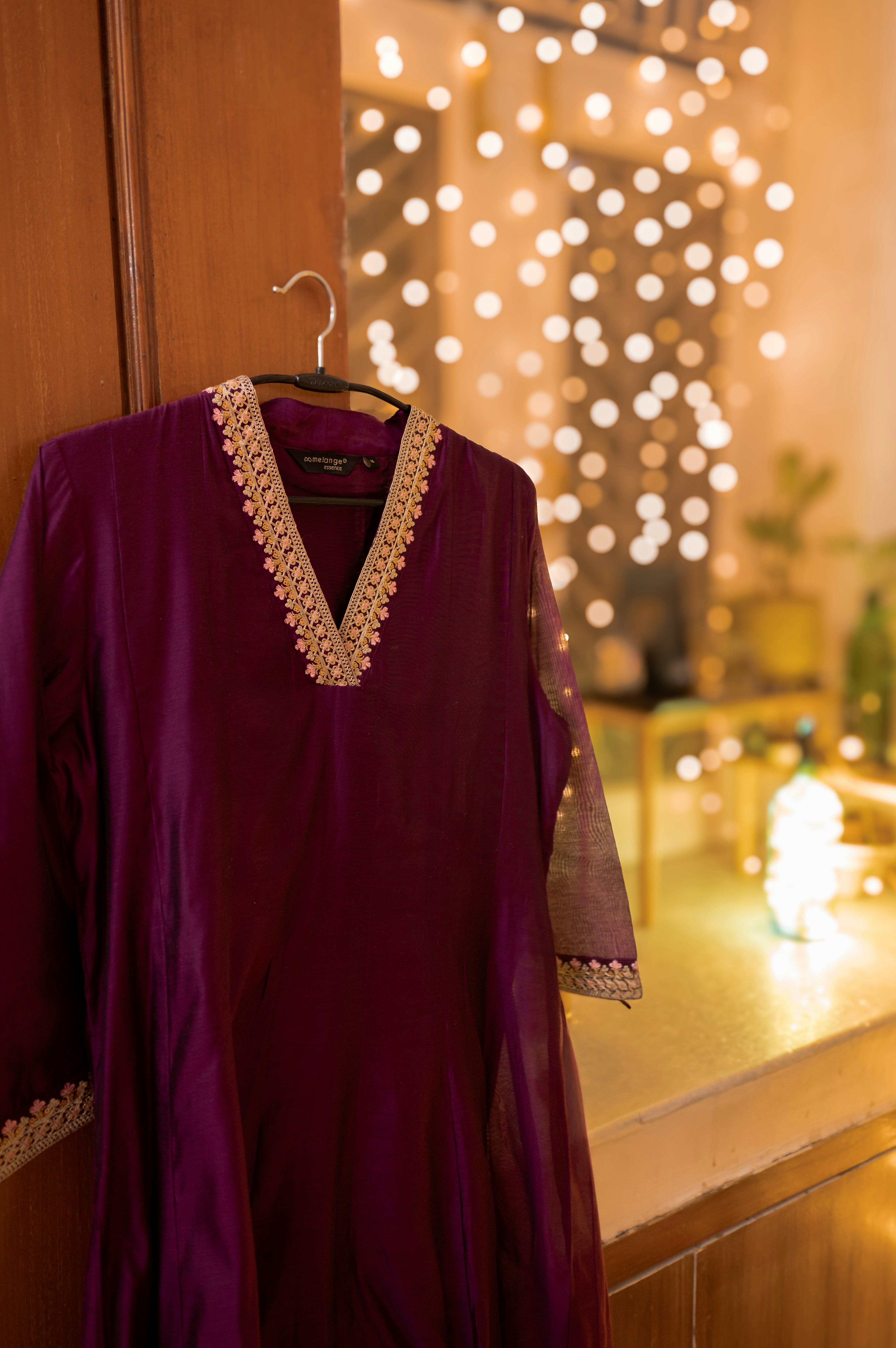 A beautifully embroidered purple garment hangs against a softly lit background adorned with twinkling lights. The intricate detailing highlights the craftsmanship of traditional attire.