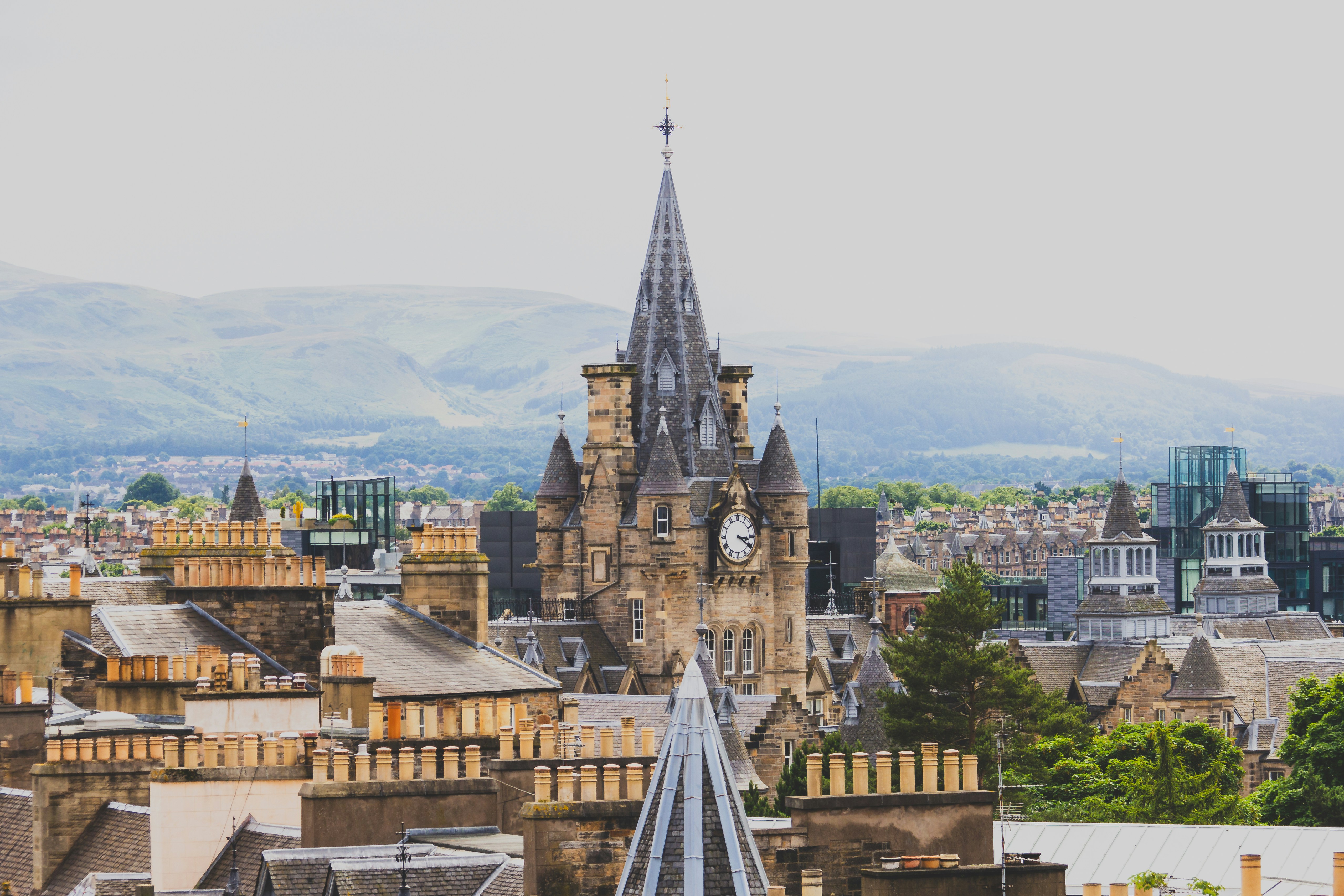 Historic Edinburgh rooftops with a prominent Gothic spire framed by distant rolling hills.