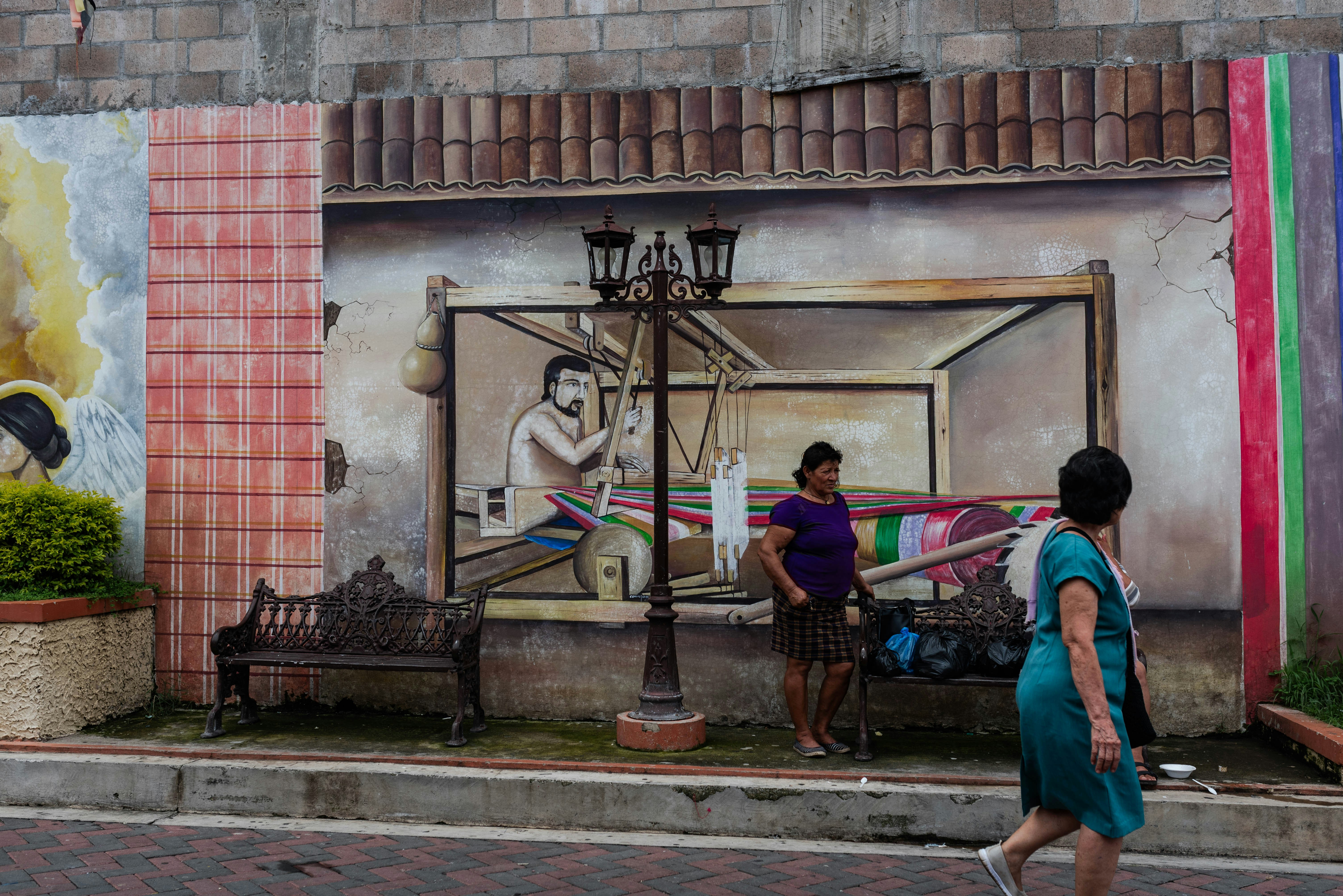 A woman walking down a street past a building with a mural on the side ...