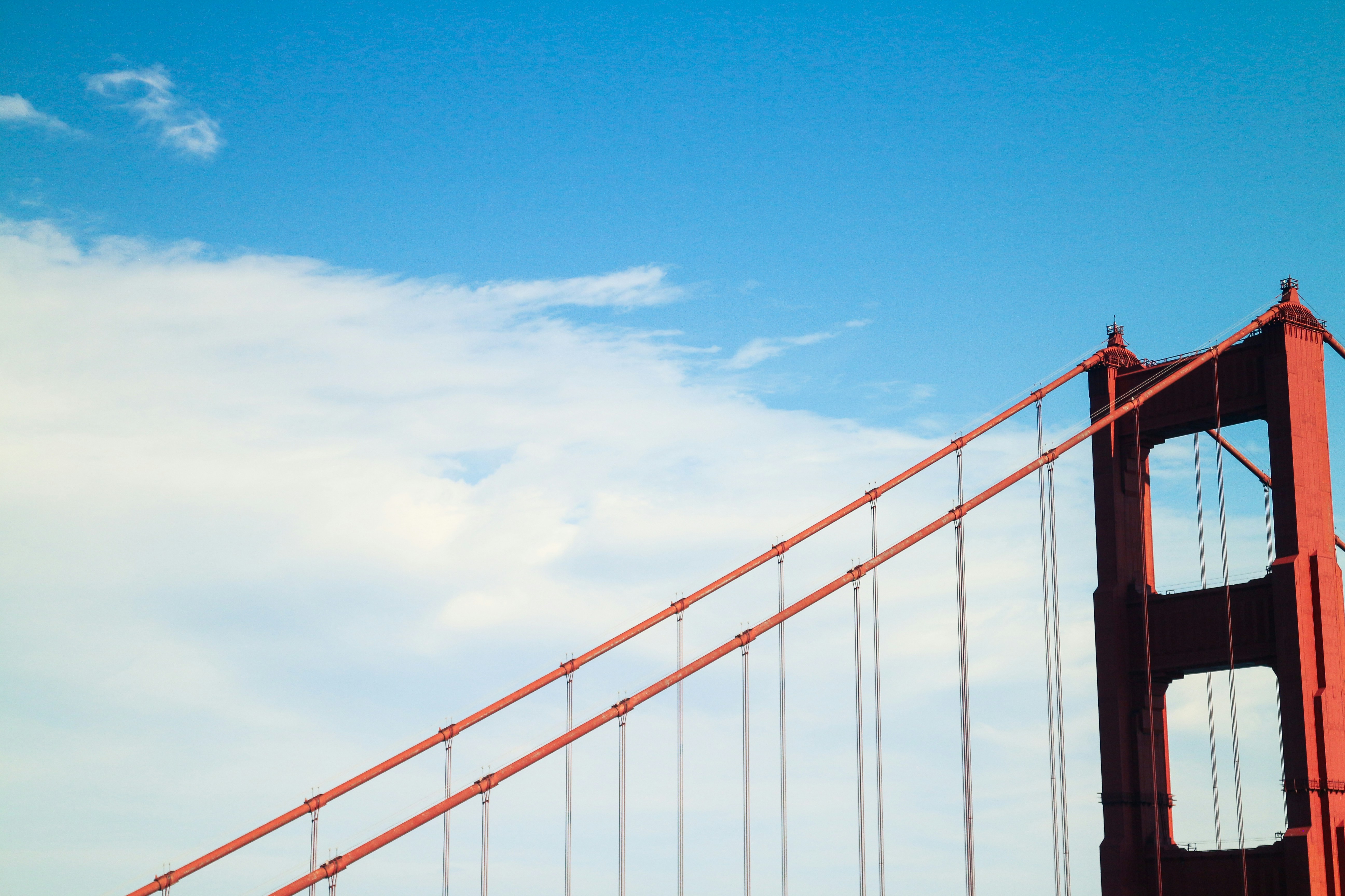 Partial view of the Golden Gate Bridge with its iconic red towers and cables set against a clear blue sky.