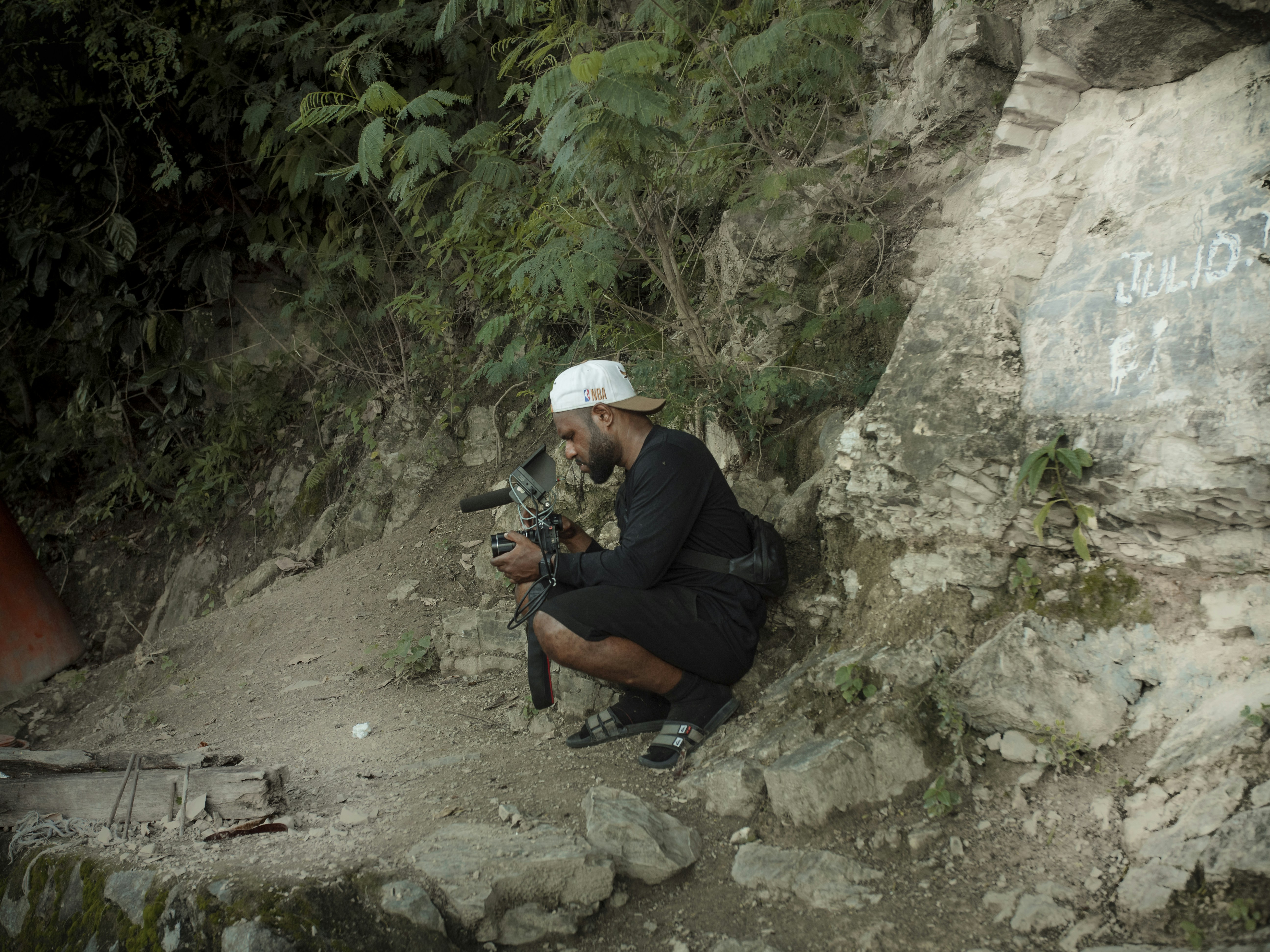 Crouched Cameraman on a Rocky Ledge, Framing a Low-Angle Moment